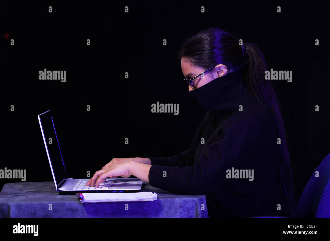 Portrait of a beautiful and smart girl hacker with laptop on dark ...