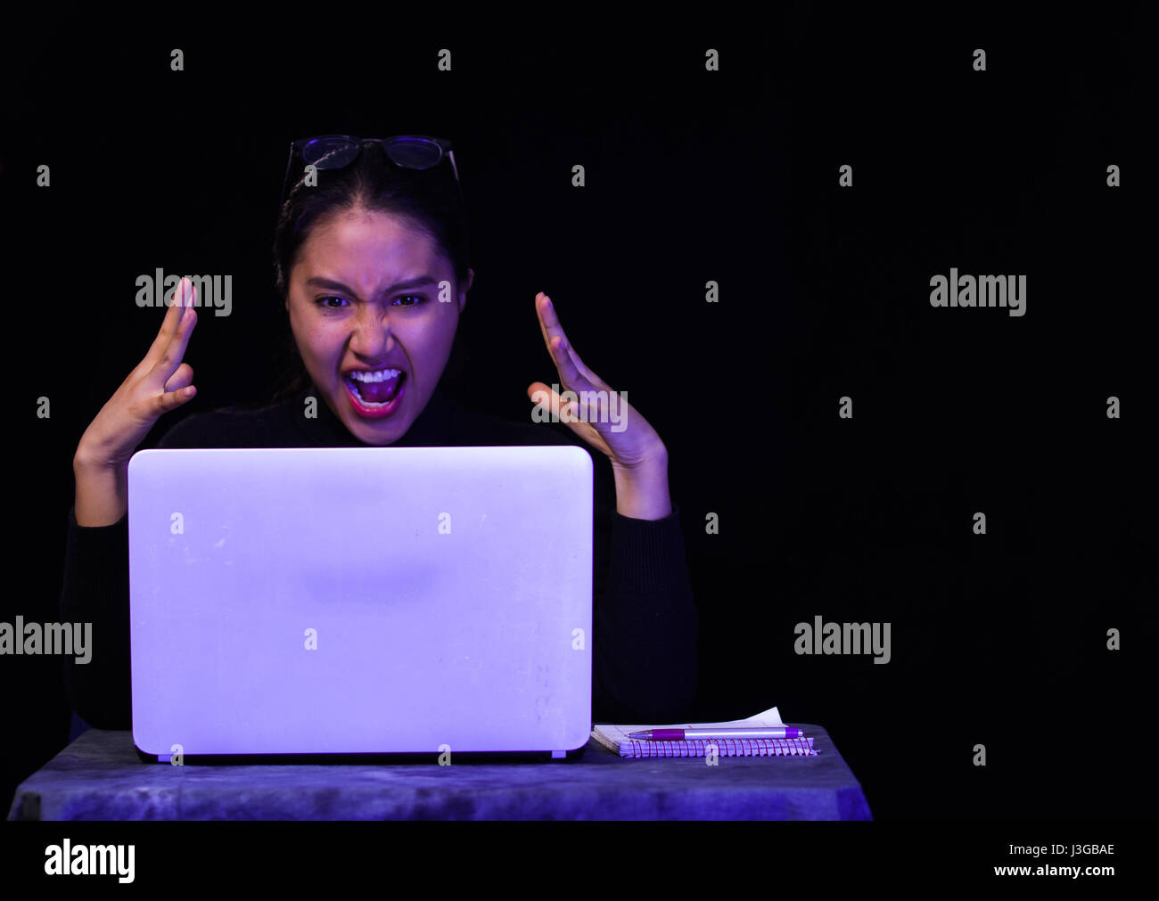Beautiful girl screaming in front of her laptop on dark background ...