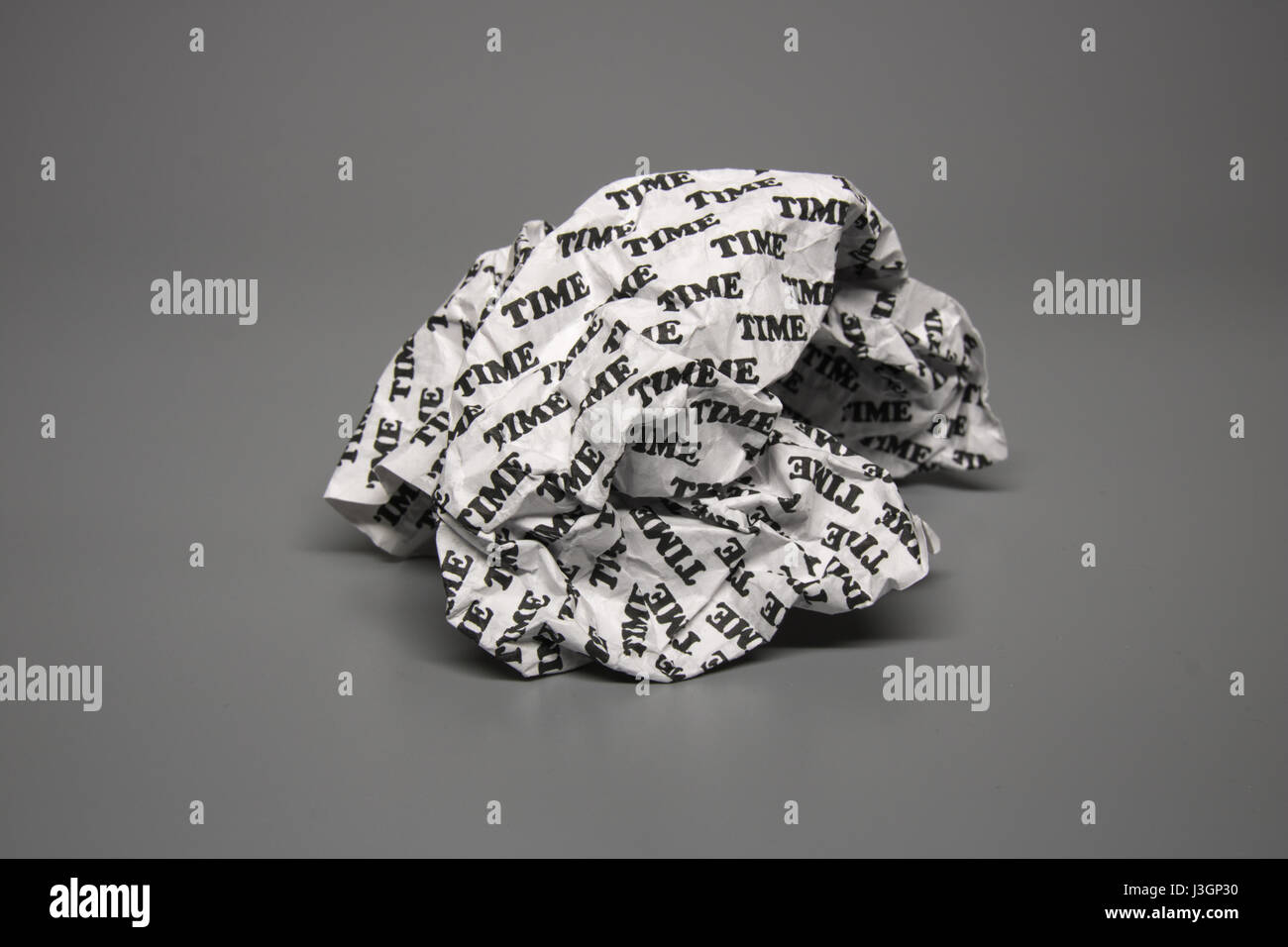 A crumpled paper with the word "time" written all over it on a grey ...
