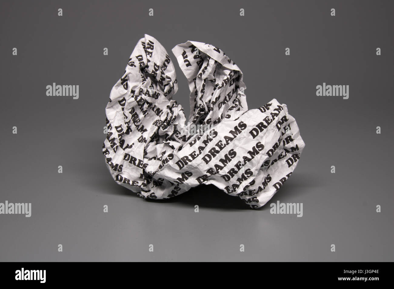A crumpled paper with the words "dreams" written all over it on a grey ...
