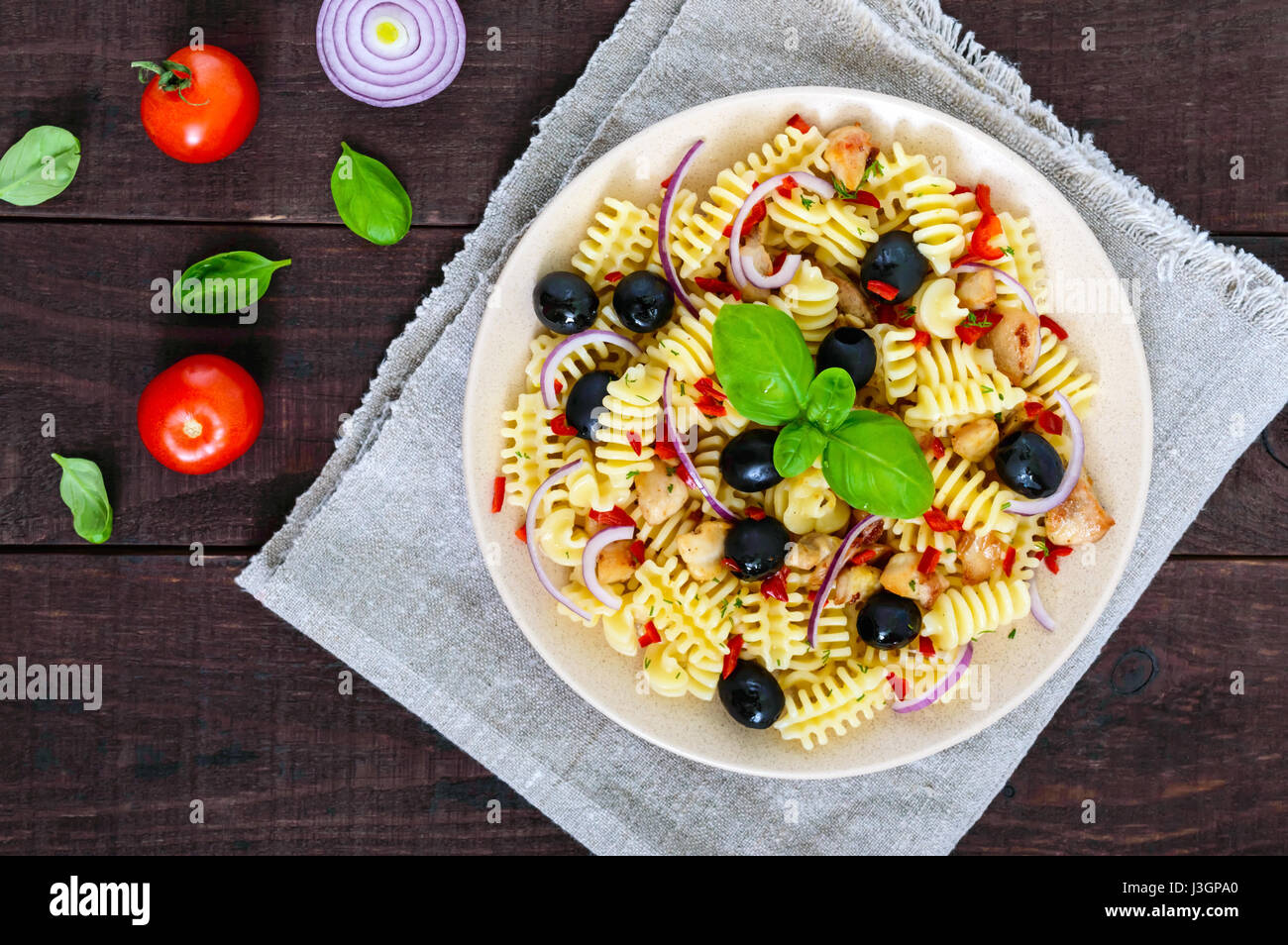 Pasta salad radiatori with chicken, black olives, blue onion, sweet pepper on a dark wooden ...
