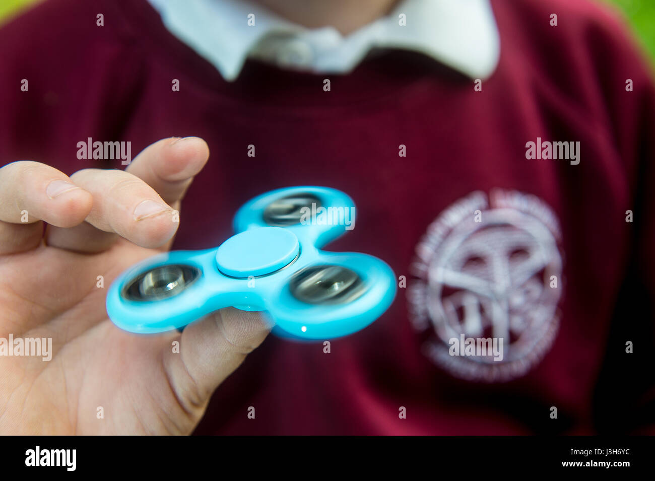 A young boy in school uniform plays with a blue fidget spinner toy ...