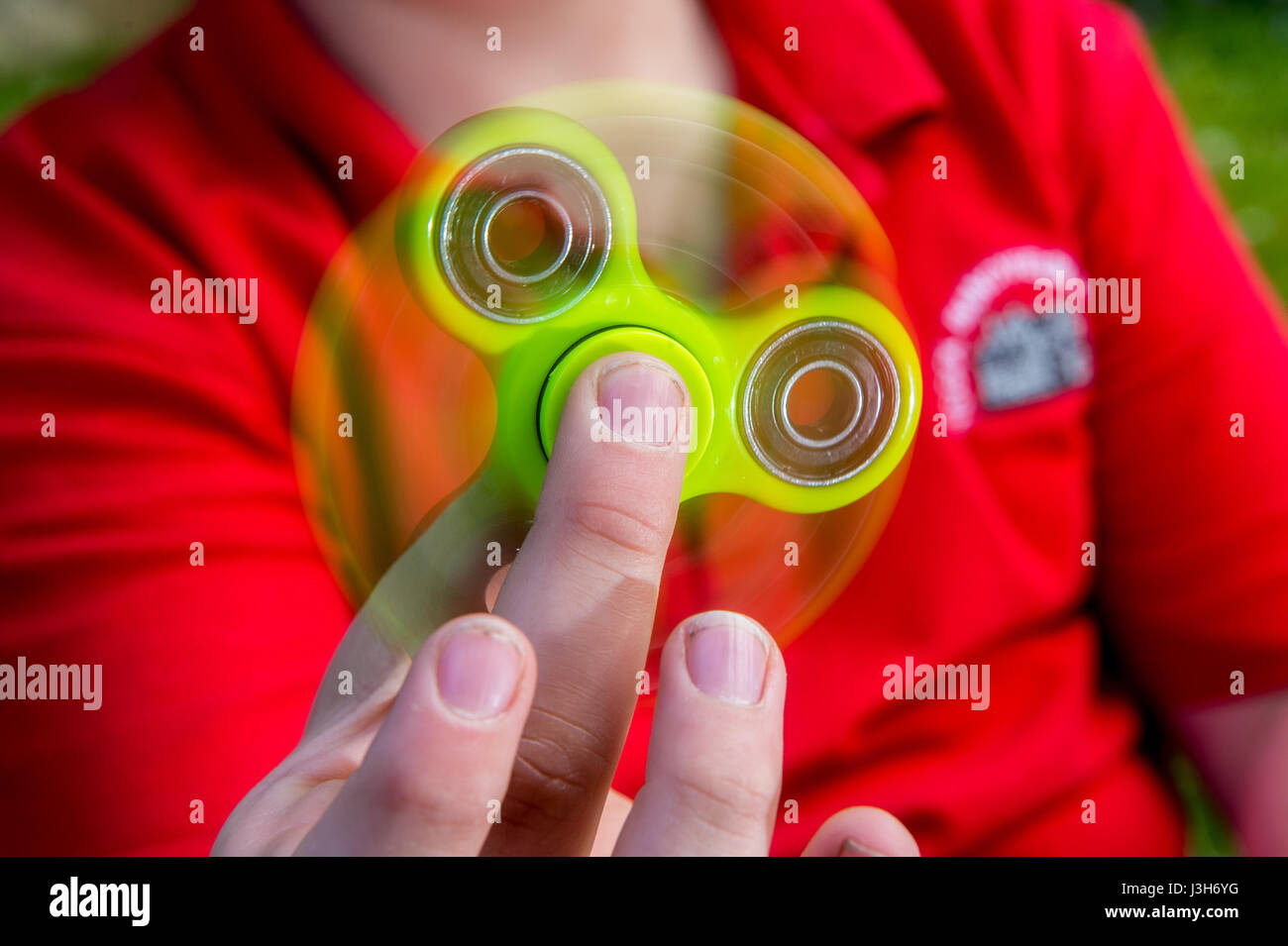A young boy in a red school uniform plays with a green fidget spinner ...
