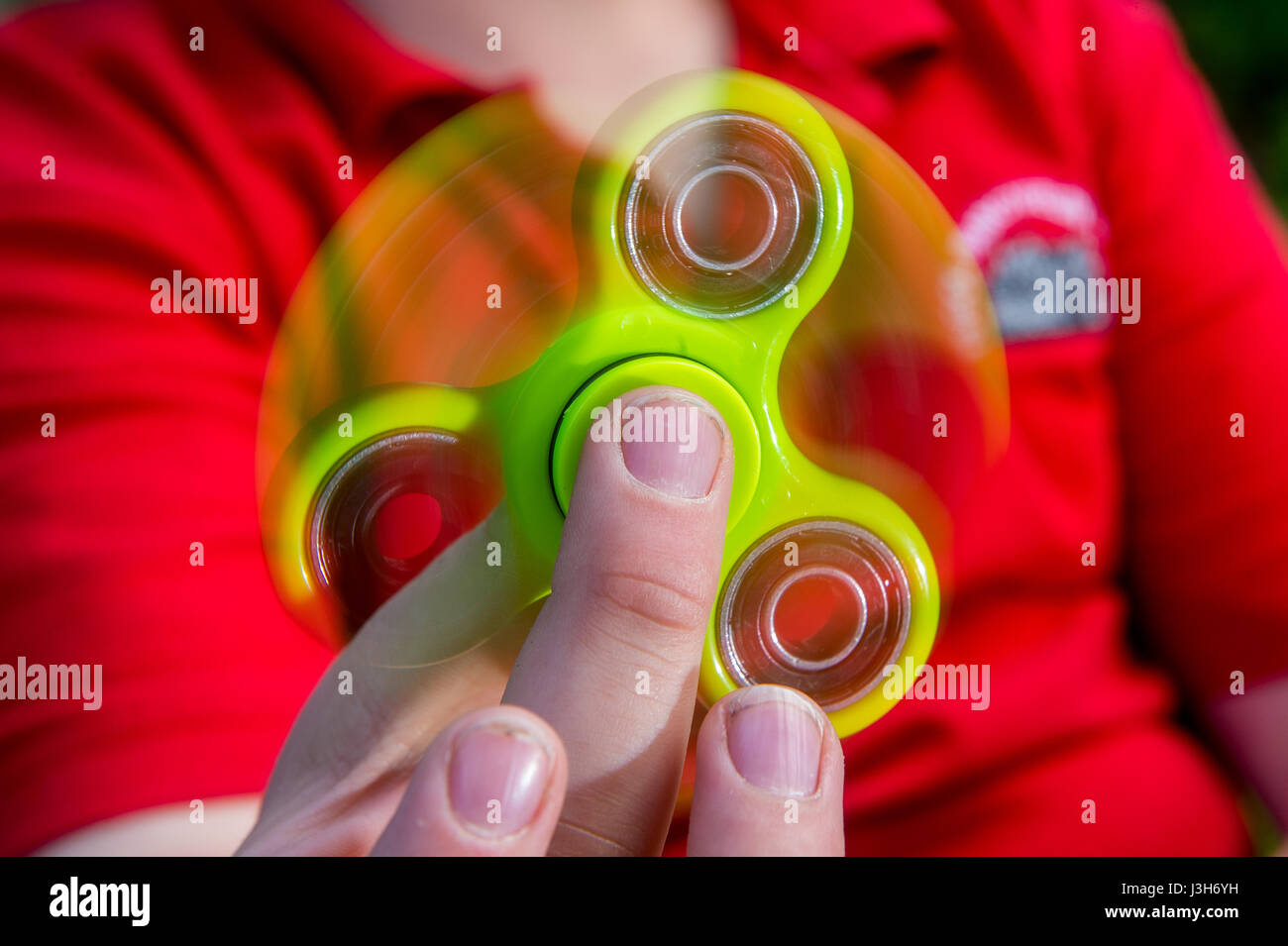 A young boy in a red school uniform plays with a green fidget spinner ...