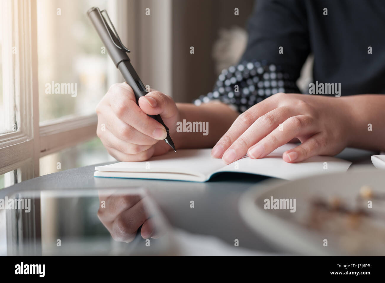 Woman hand holding pen while writing on small notebook beside window ...