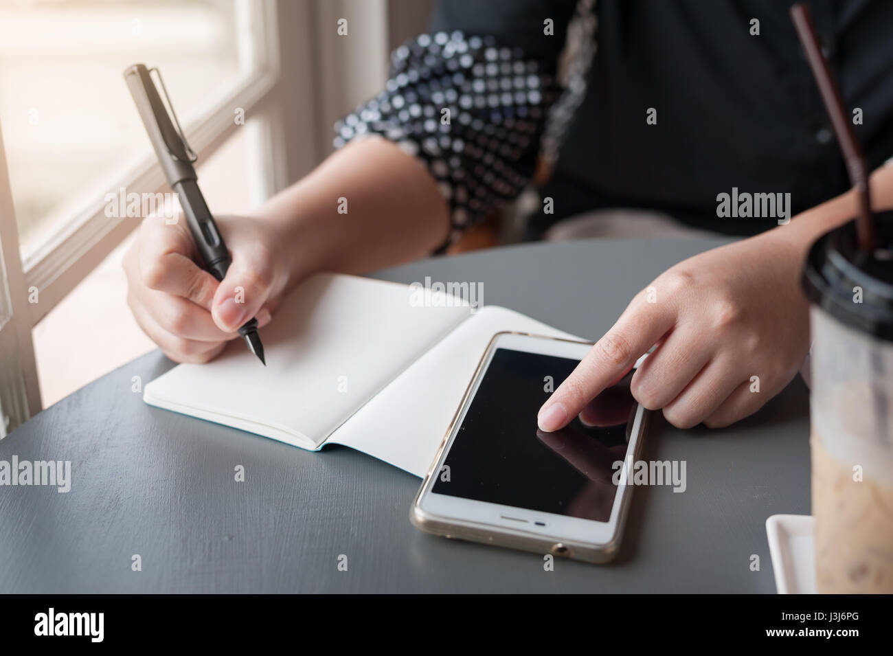Woman hand writing a note on notebook while another hand touching on ...
