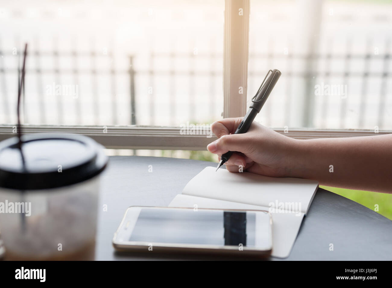 Woman hand holding pen while writing on small notebook with smartphone ...