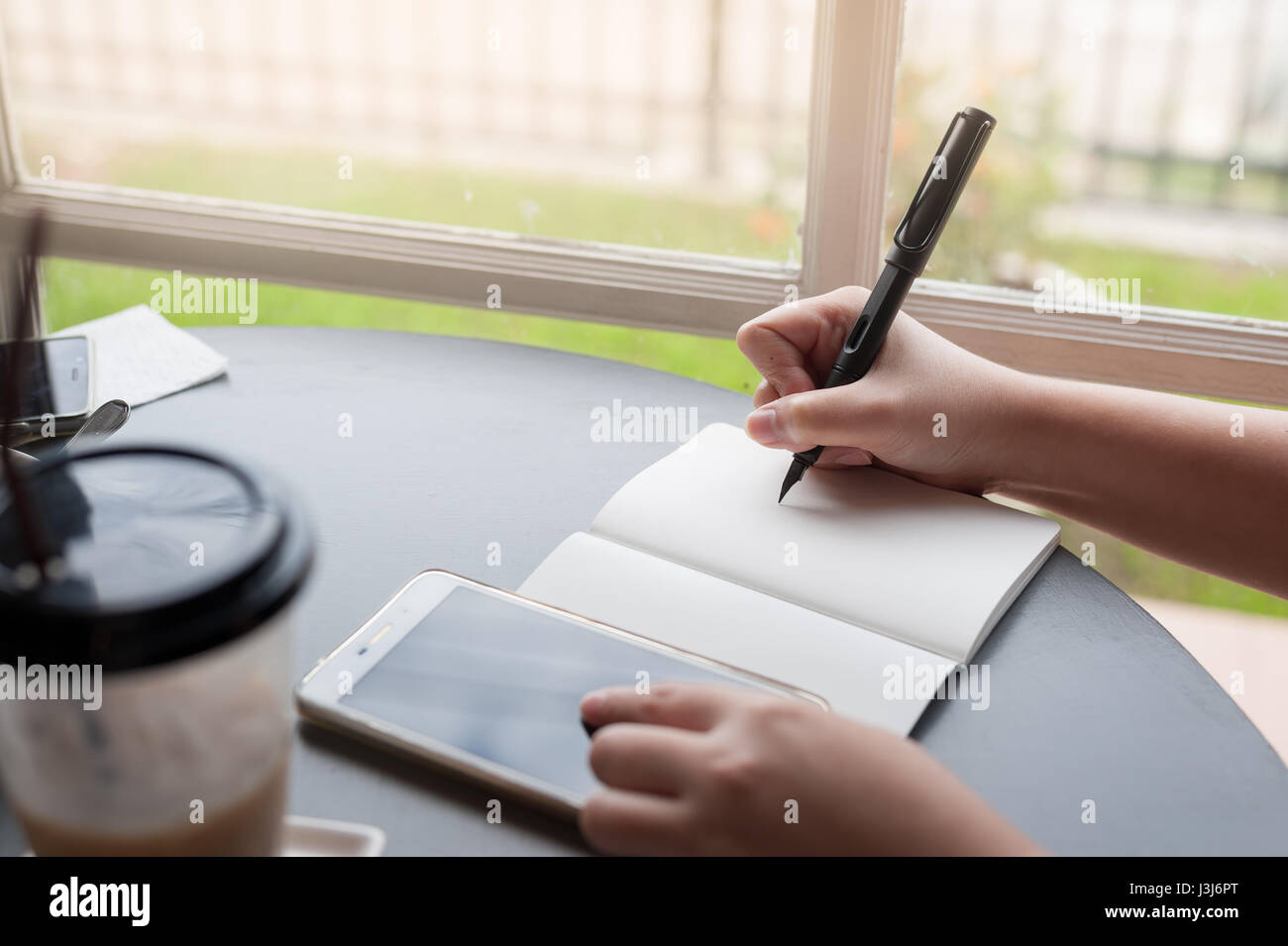 Woman hand writing a note on notebook while another hand touching on ...