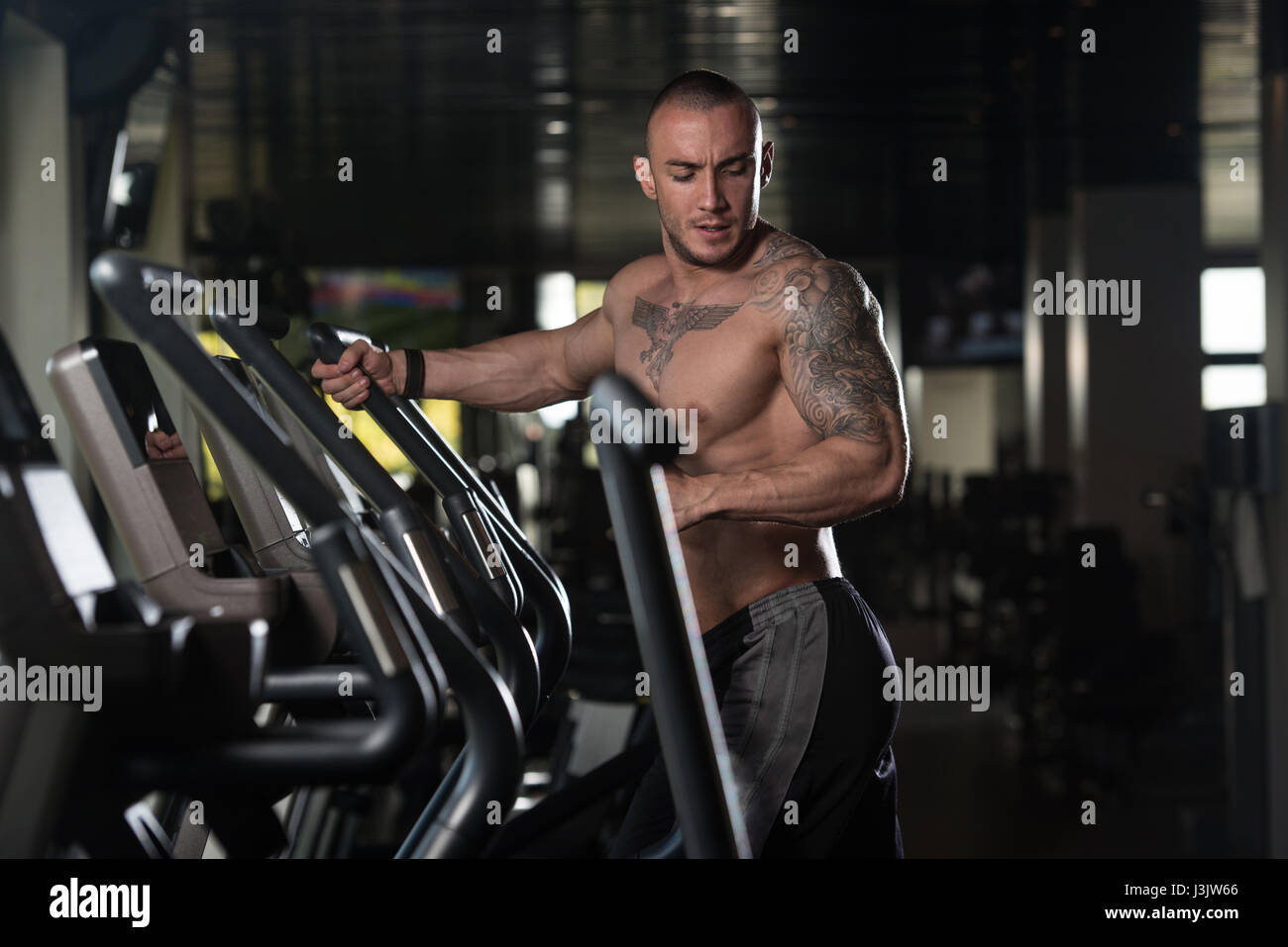 Muscular Young Man Doing Aerobics Elliptical Walker In Modern Fitness ...