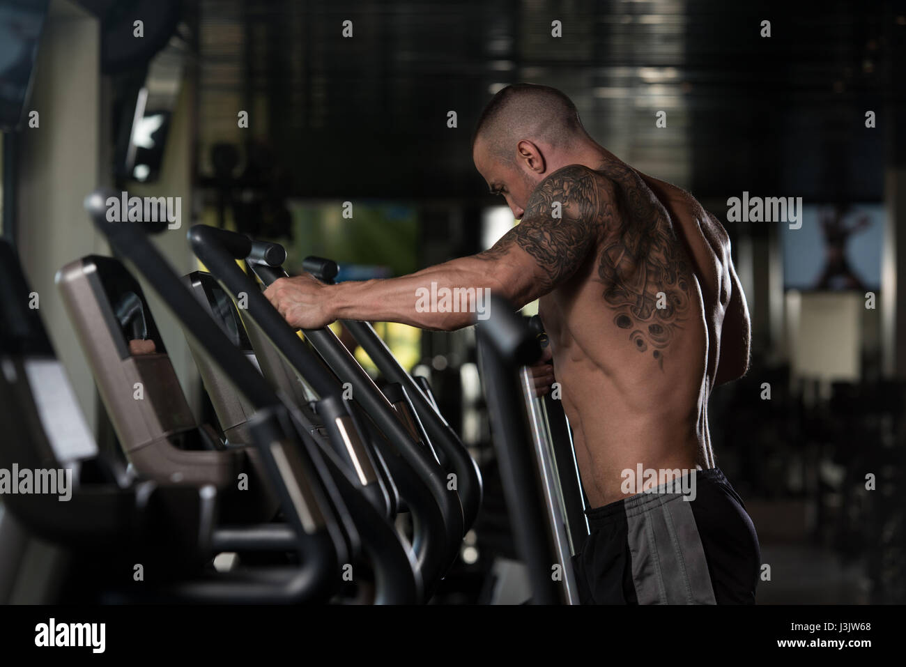 Muscular Young Man Doing Aerobics Elliptical Walker In Modern Fitness ...