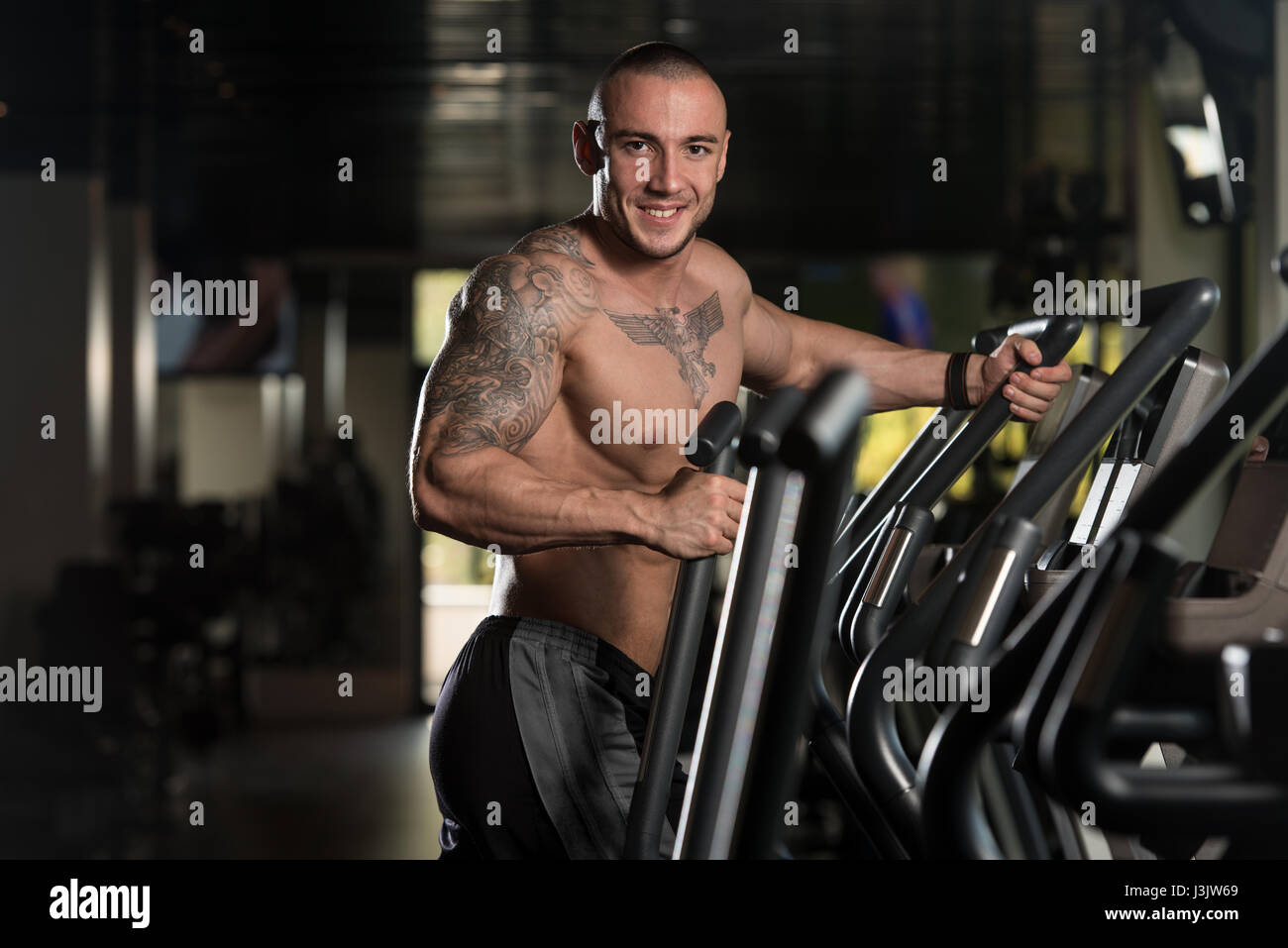Muscular Young Man Doing Aerobics Elliptical Walker In Modern Fitness ...