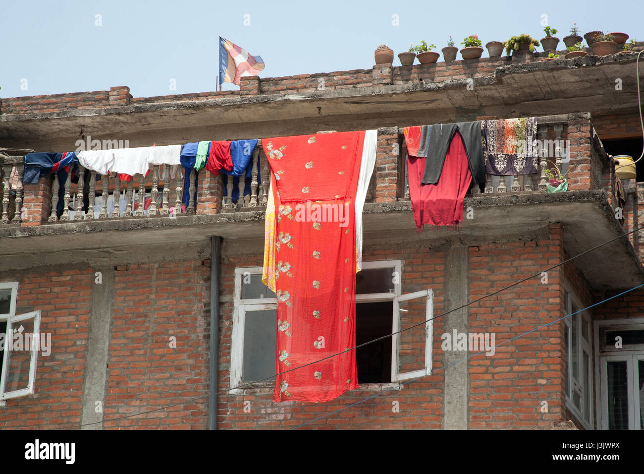 Bright red sari fabric hanging to dry from a roof with other washing ...