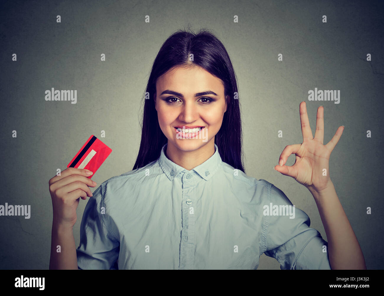 Happy woman with credit card showing ok sign isolated on gray wall ...