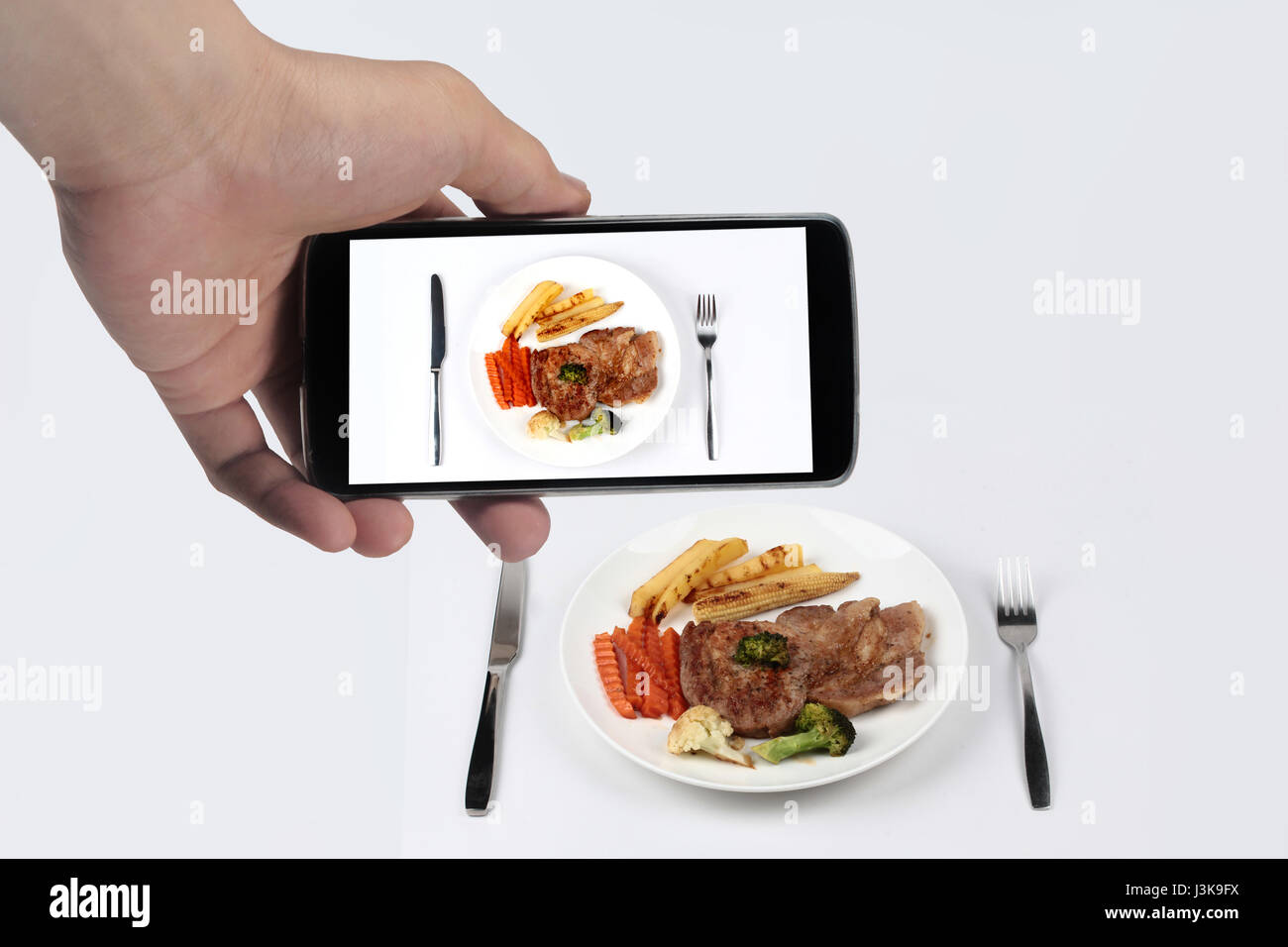 Using mobile phone to take photo pork steak with mixed vegetable for ...