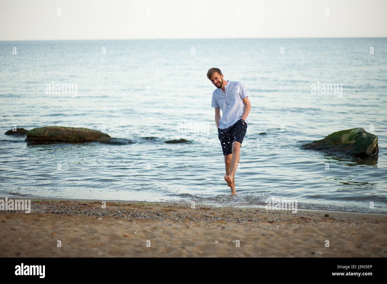 Smiling young man splashes water on beach. He cheerfully laughs and ...