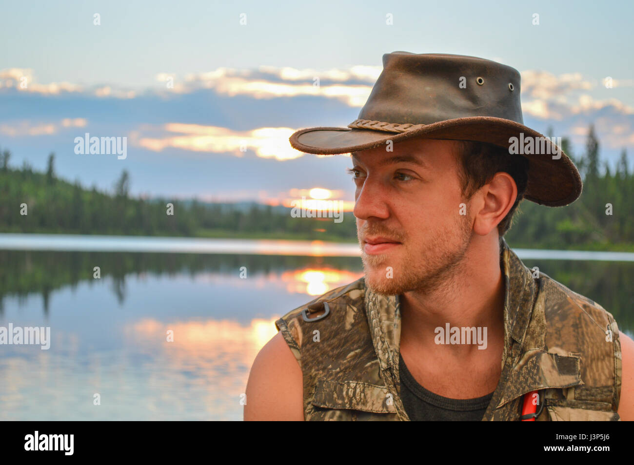 Handsome young fisherman on a lake wearing a leather hat and safety ...