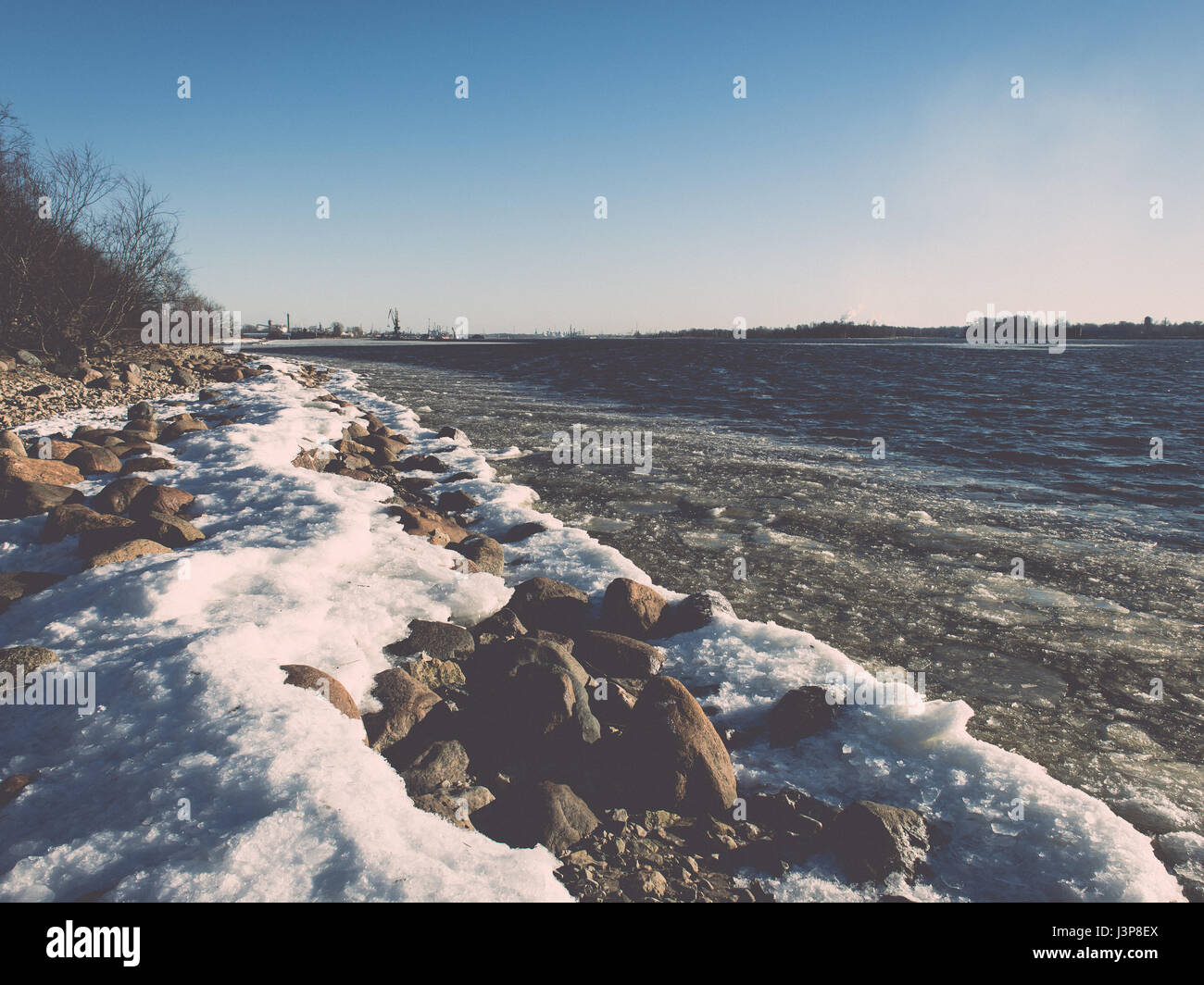 frozen beach near shipyard and sea port with rays of sun and ...