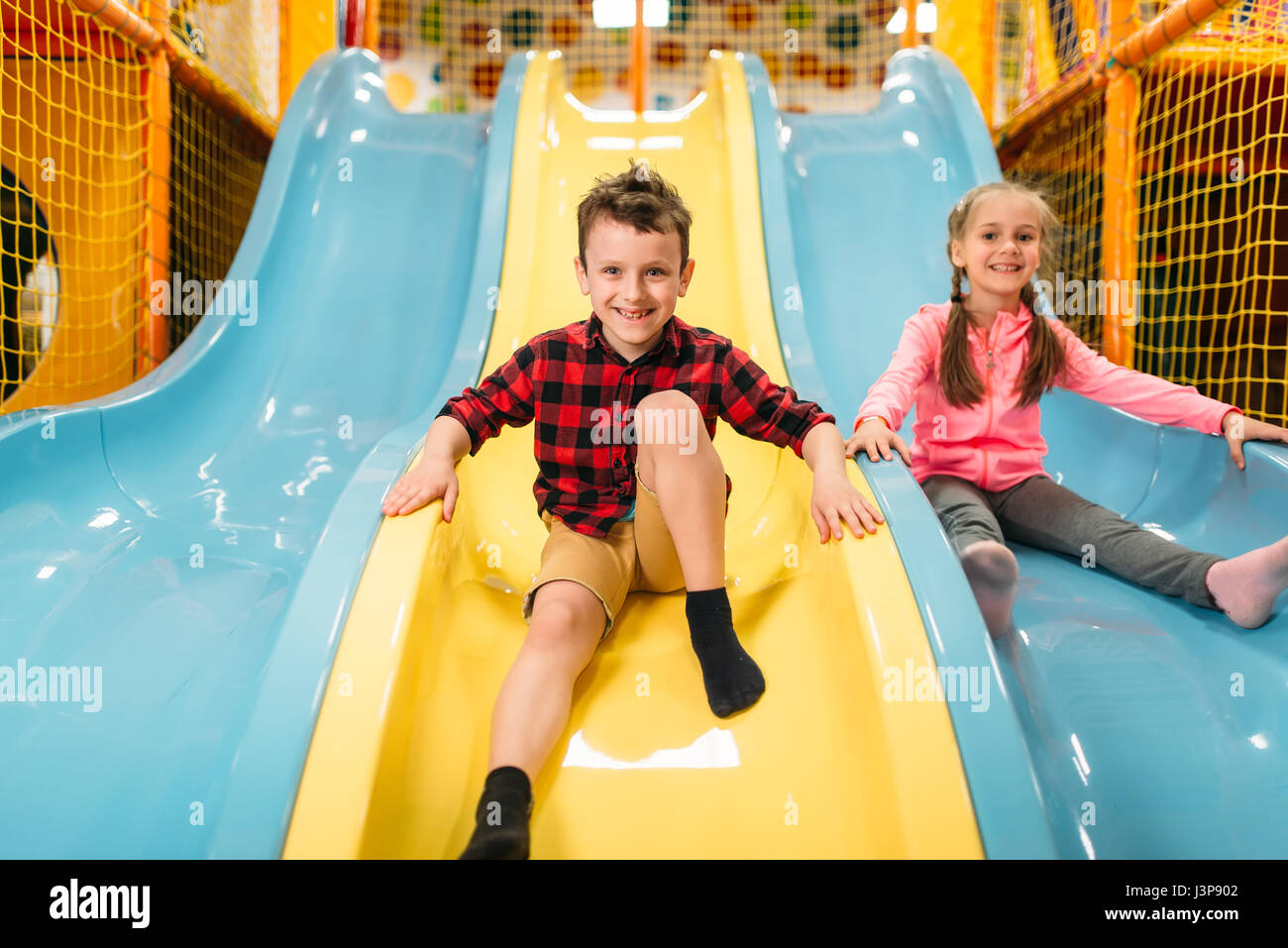 Little kids riding from childrens slides in game center. Happy ...