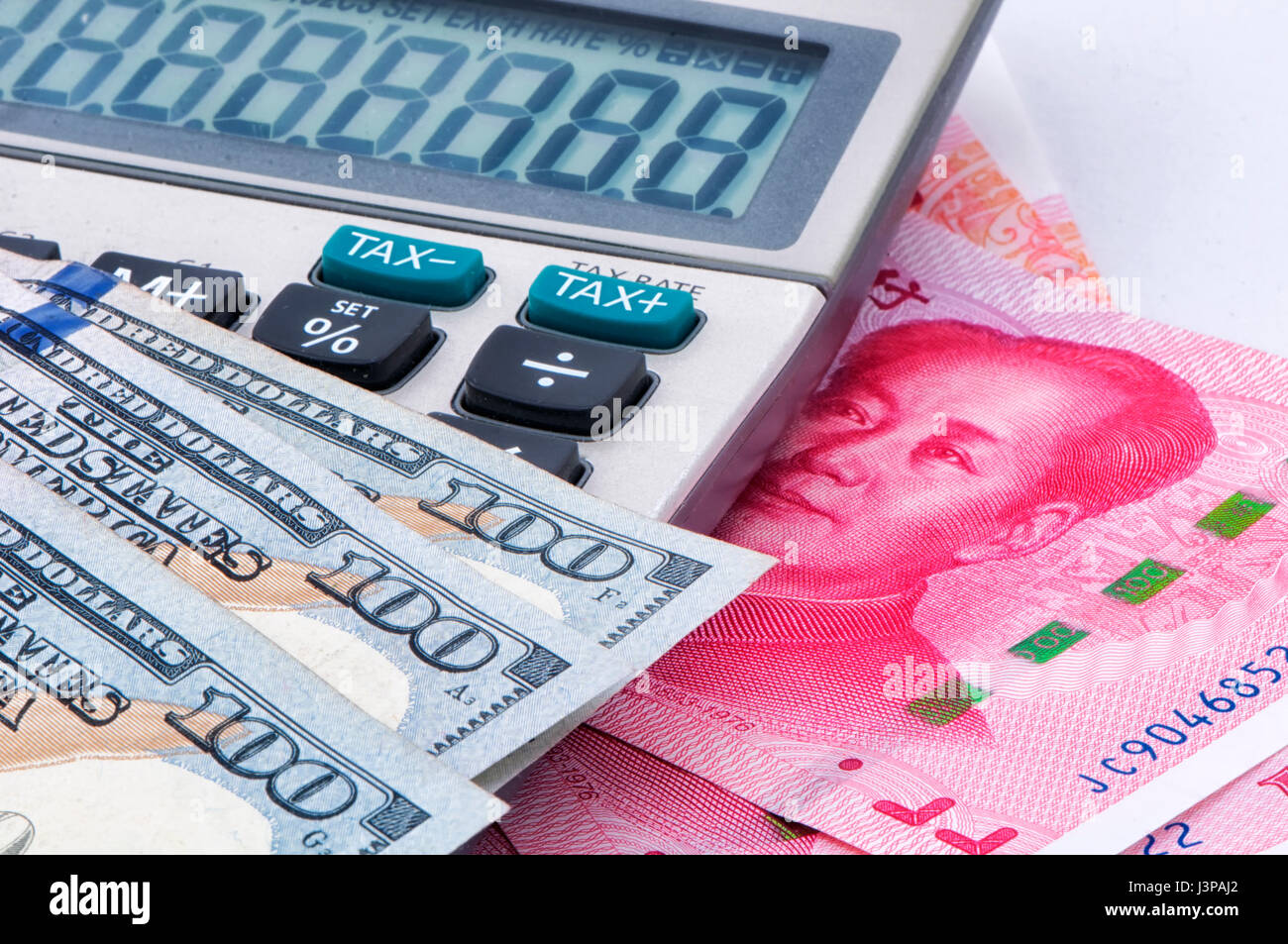 Chinese 100 Renminbi and 100 U.S. dollar bills piled on a white ...