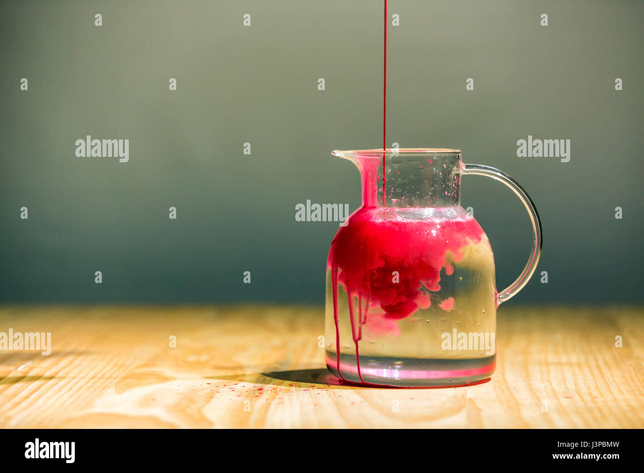 Red paint falling into a glass pitcher filled with water Stock Photo ...