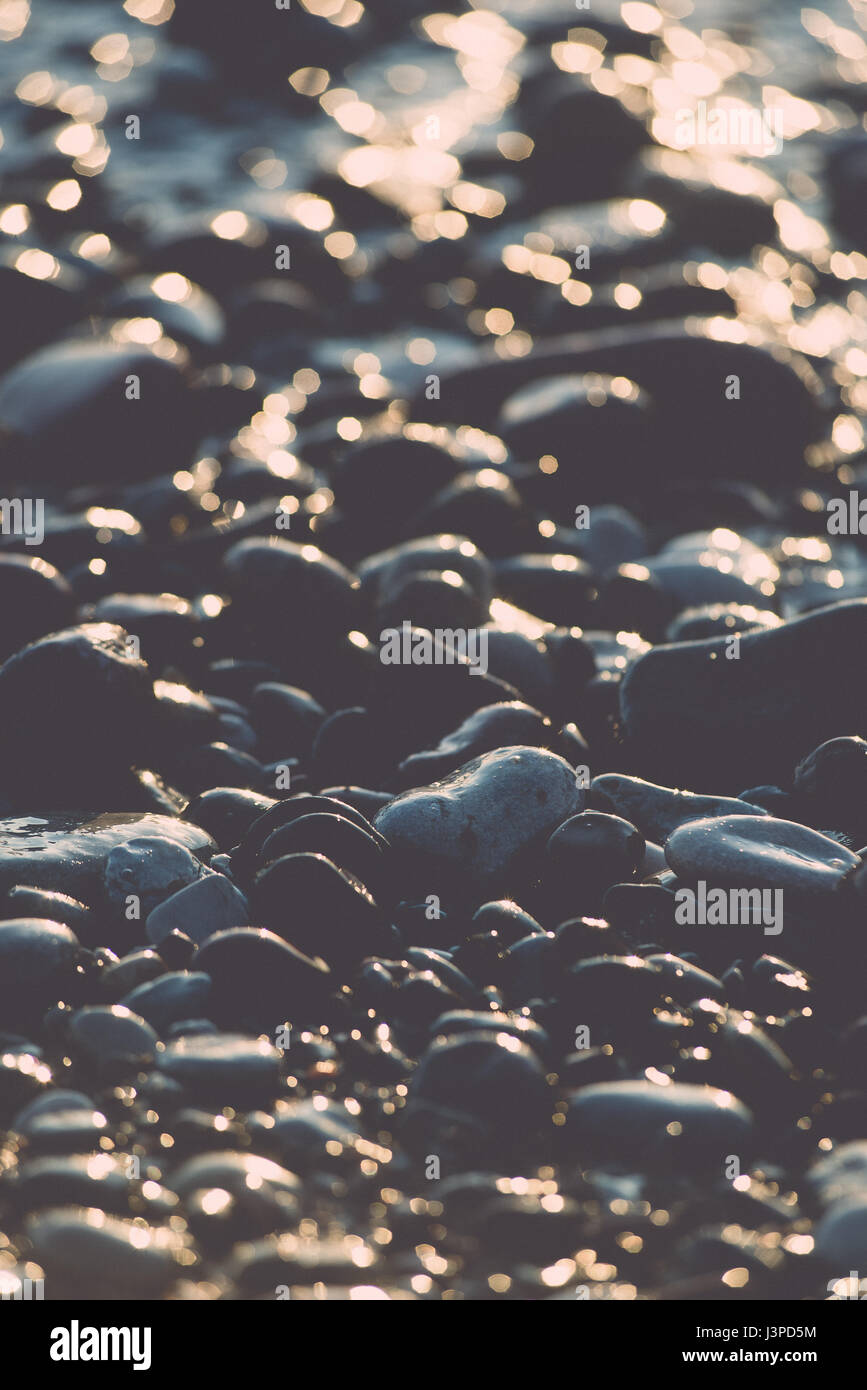 sun reflections on Stones on the beach and sea water in sunset light ...