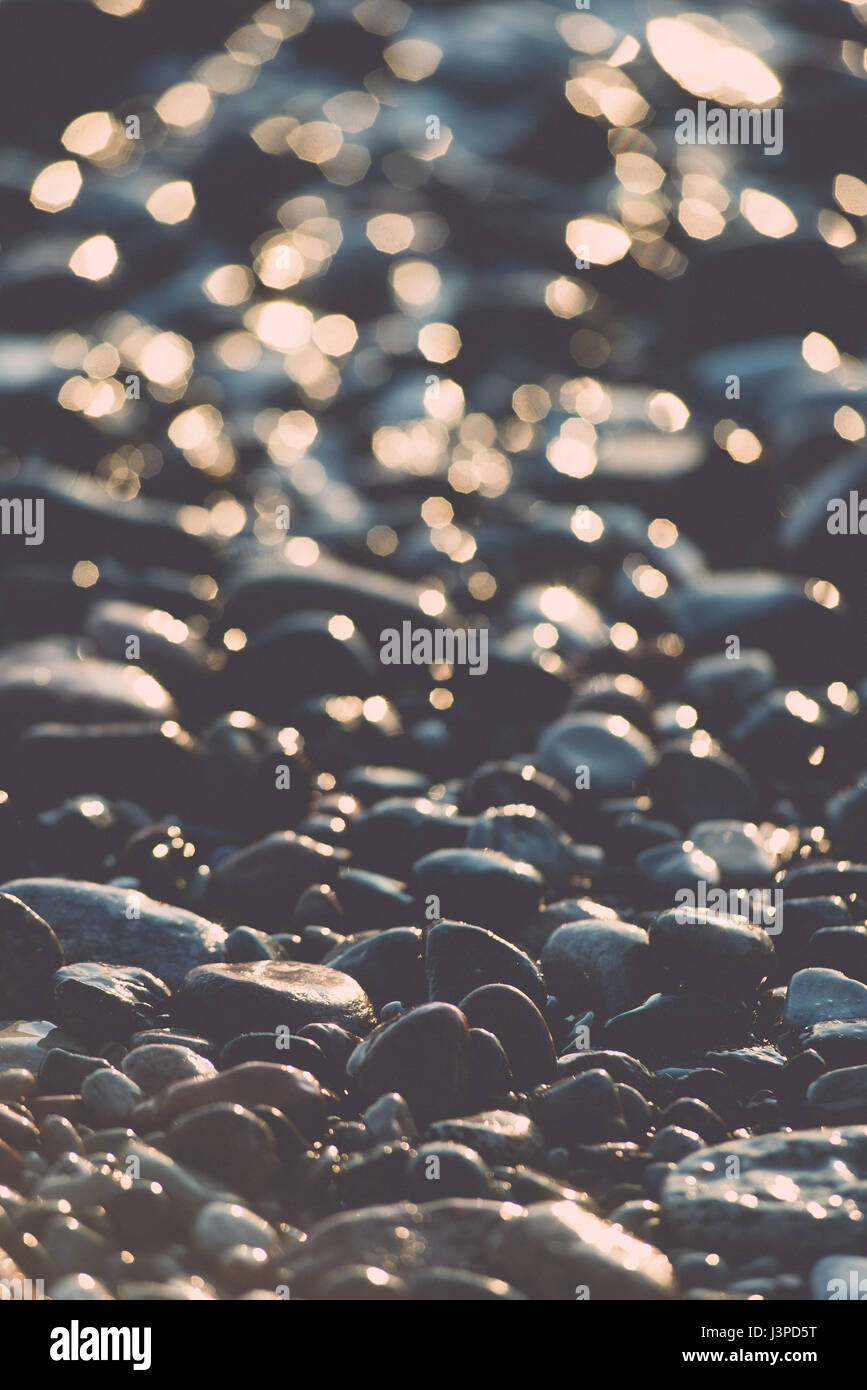 sun reflections on Stones on the beach and sea water in sunset light ...