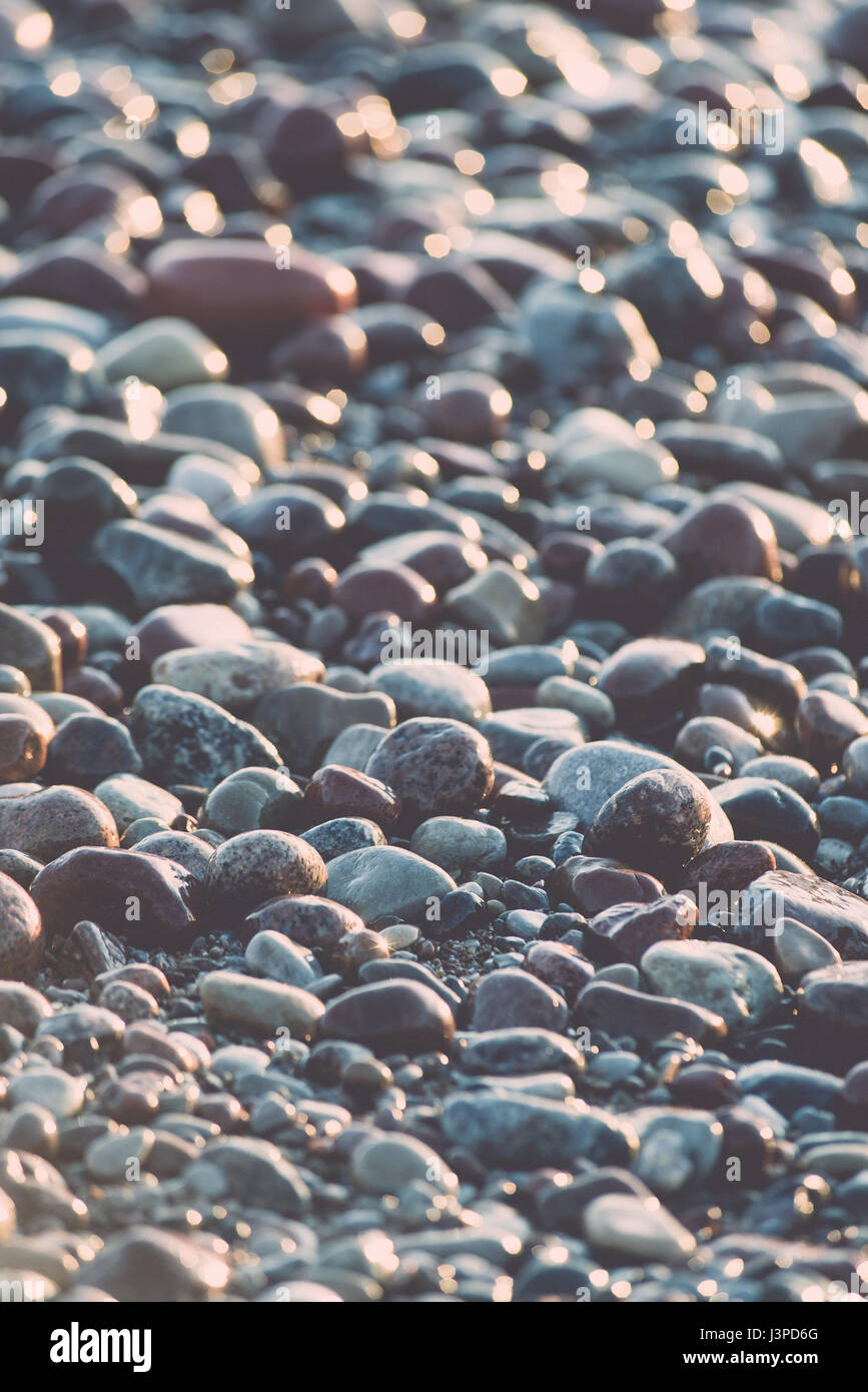 sun reflections on Stones on the beach and sea water in sunset light ...