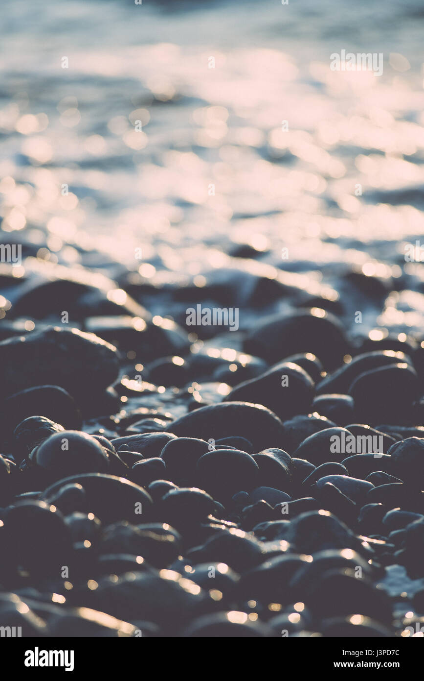 sun reflections on Stones on the beach and sea water in sunset light ...
