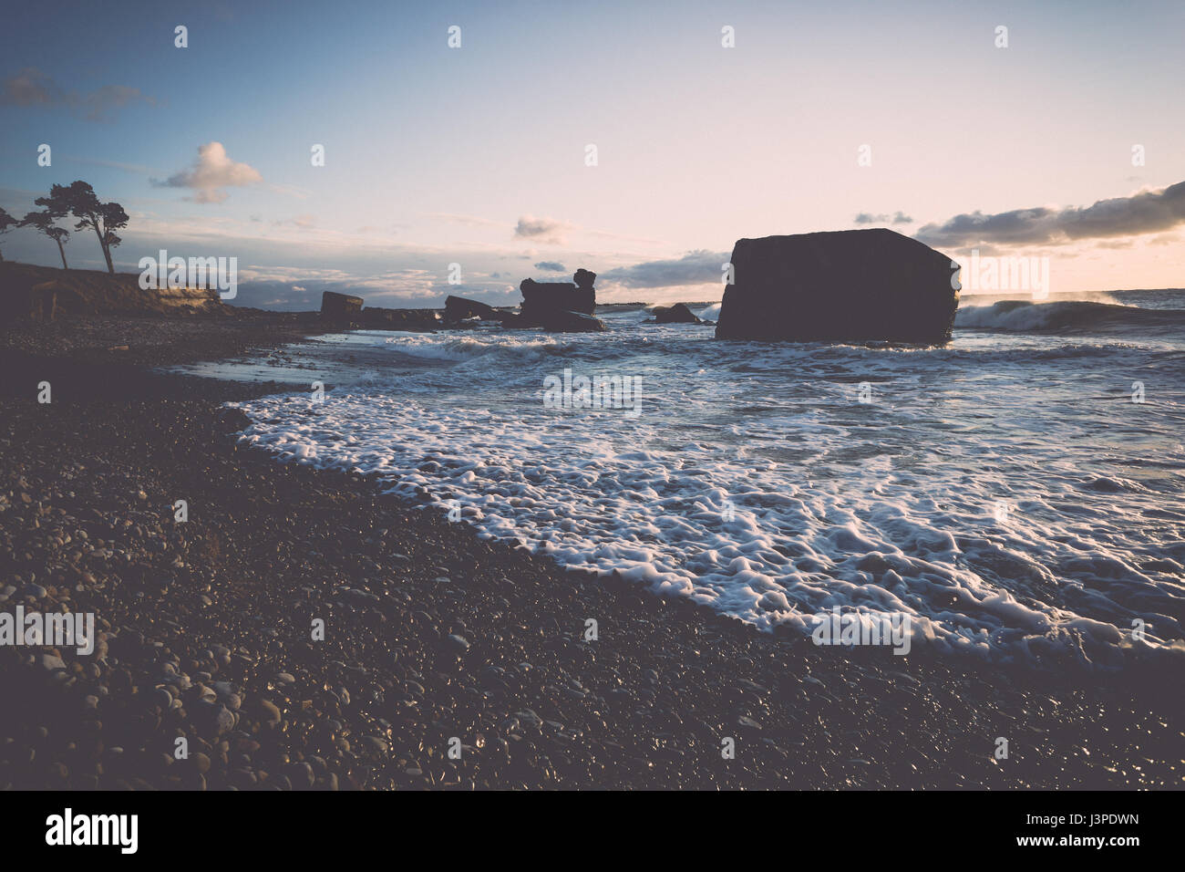 waves crushing over rocks and ruins of old fort at sunset on the beach ...