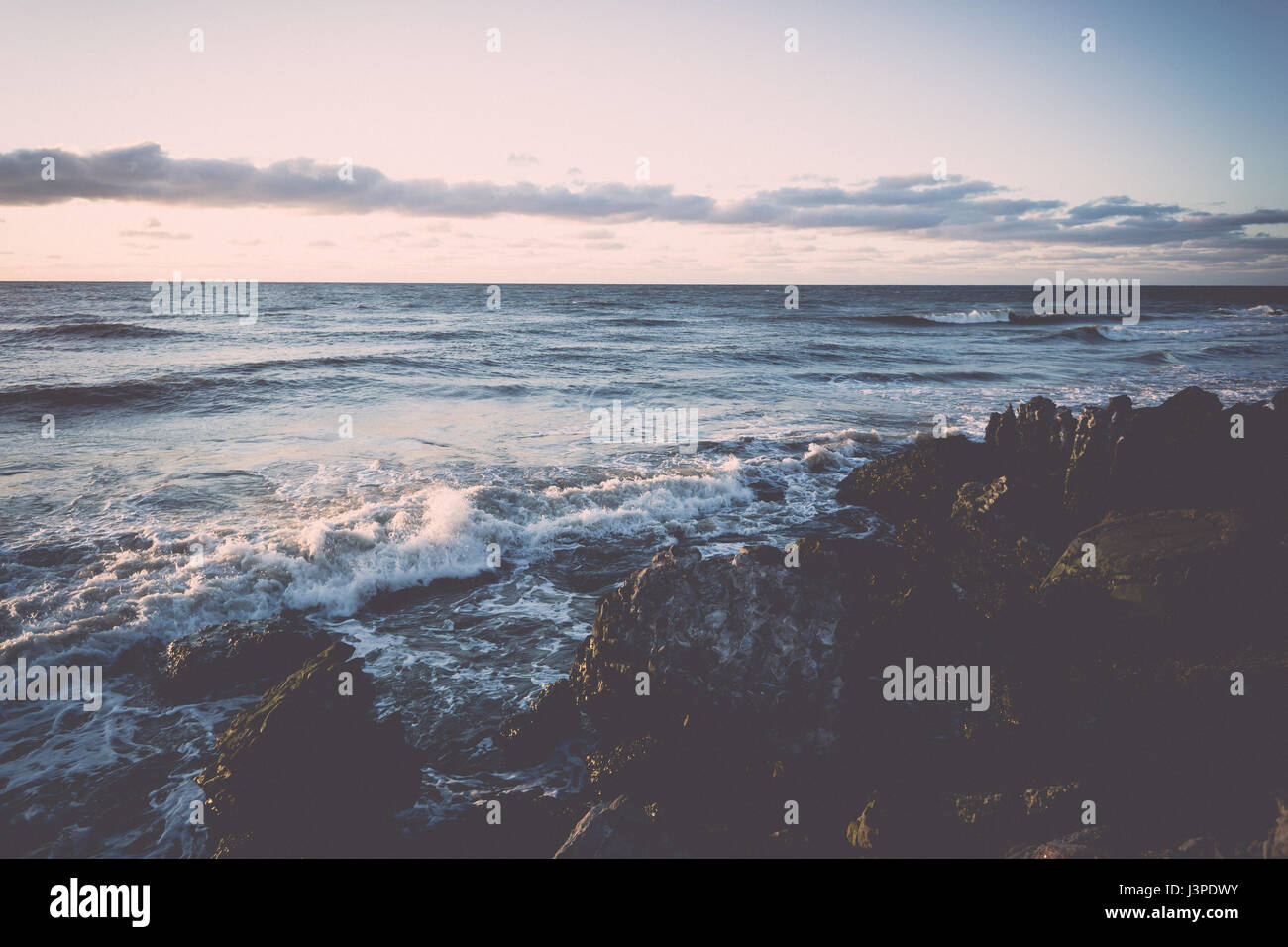 waves crushing over rocks and ruins of old fort at sunset on the beach ...
