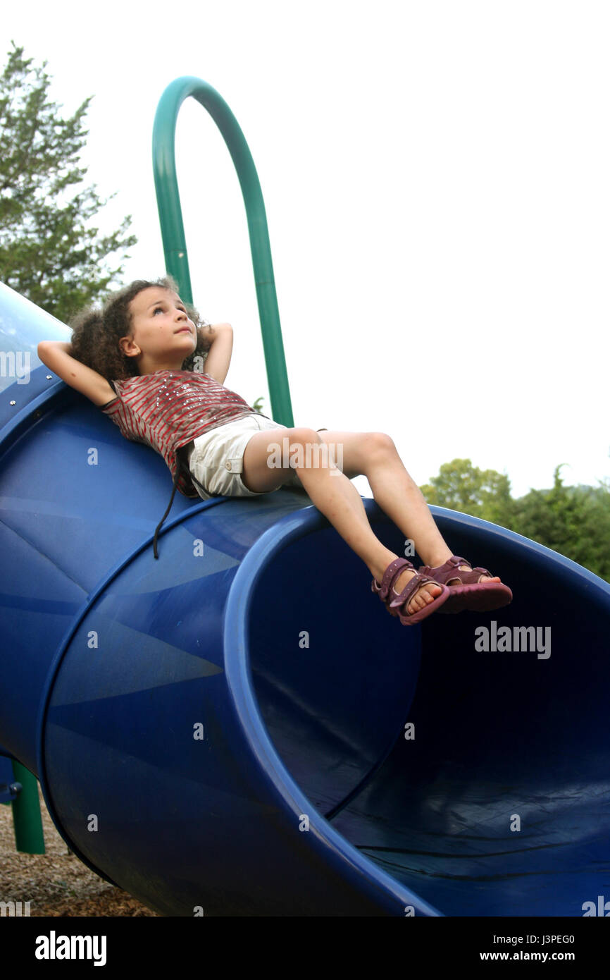 Little girl sitting on blue slide at playground Stock Photo - Alamy