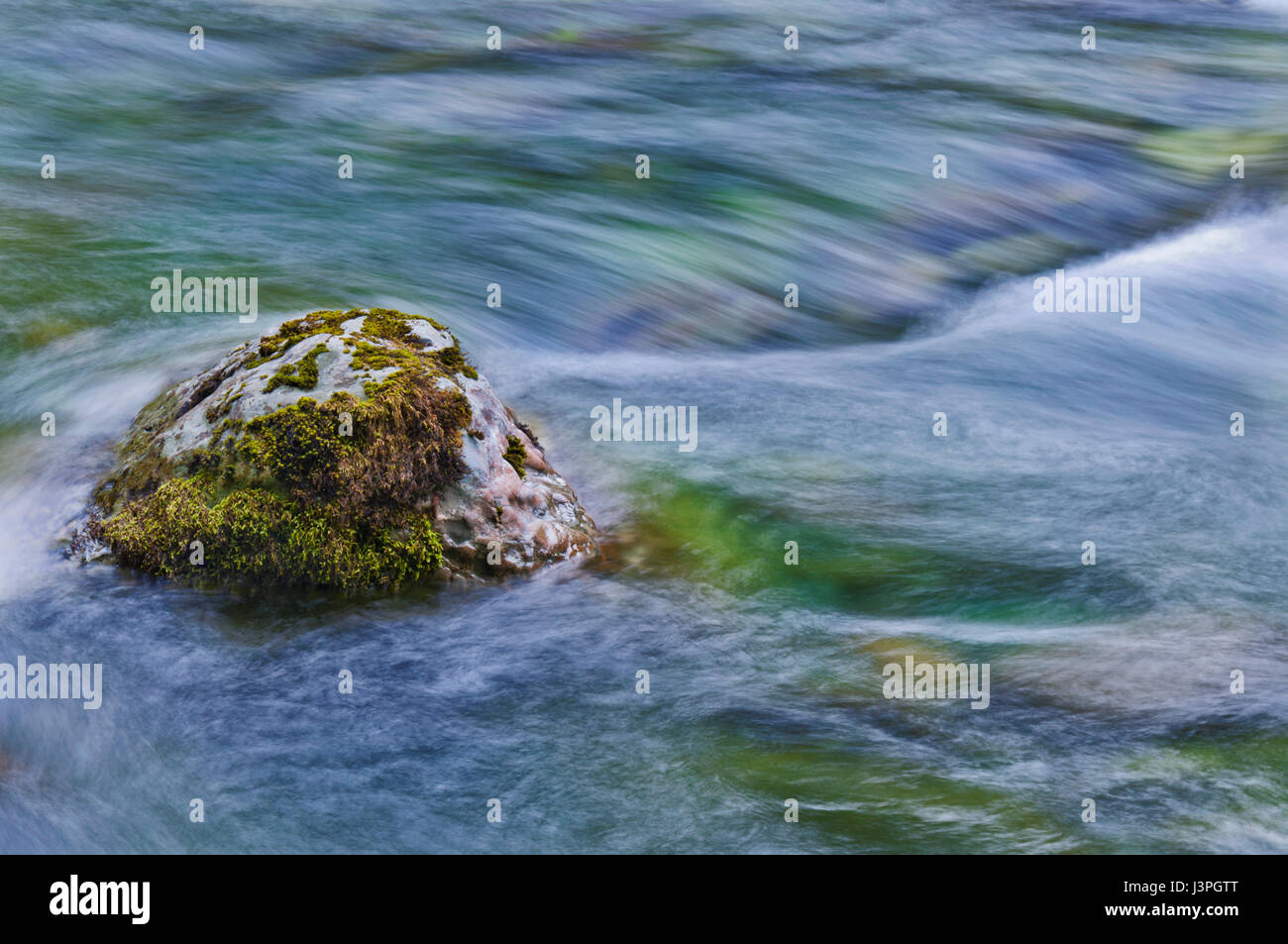 Closeup of flowing water around rock with sea green and blue colors ...