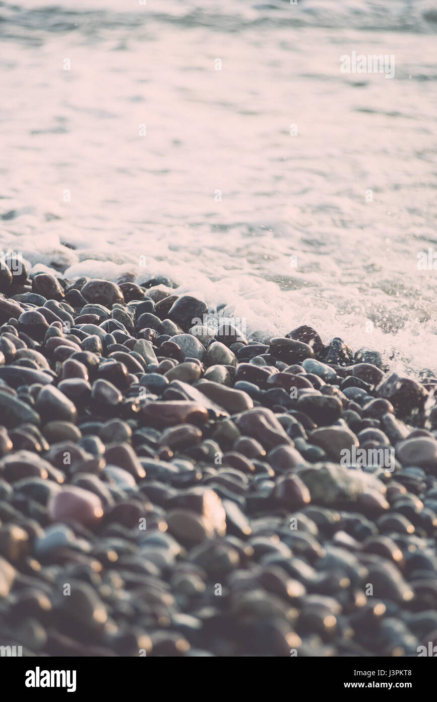 sun reflections on Stones on the beach and sea water in sunset light ...