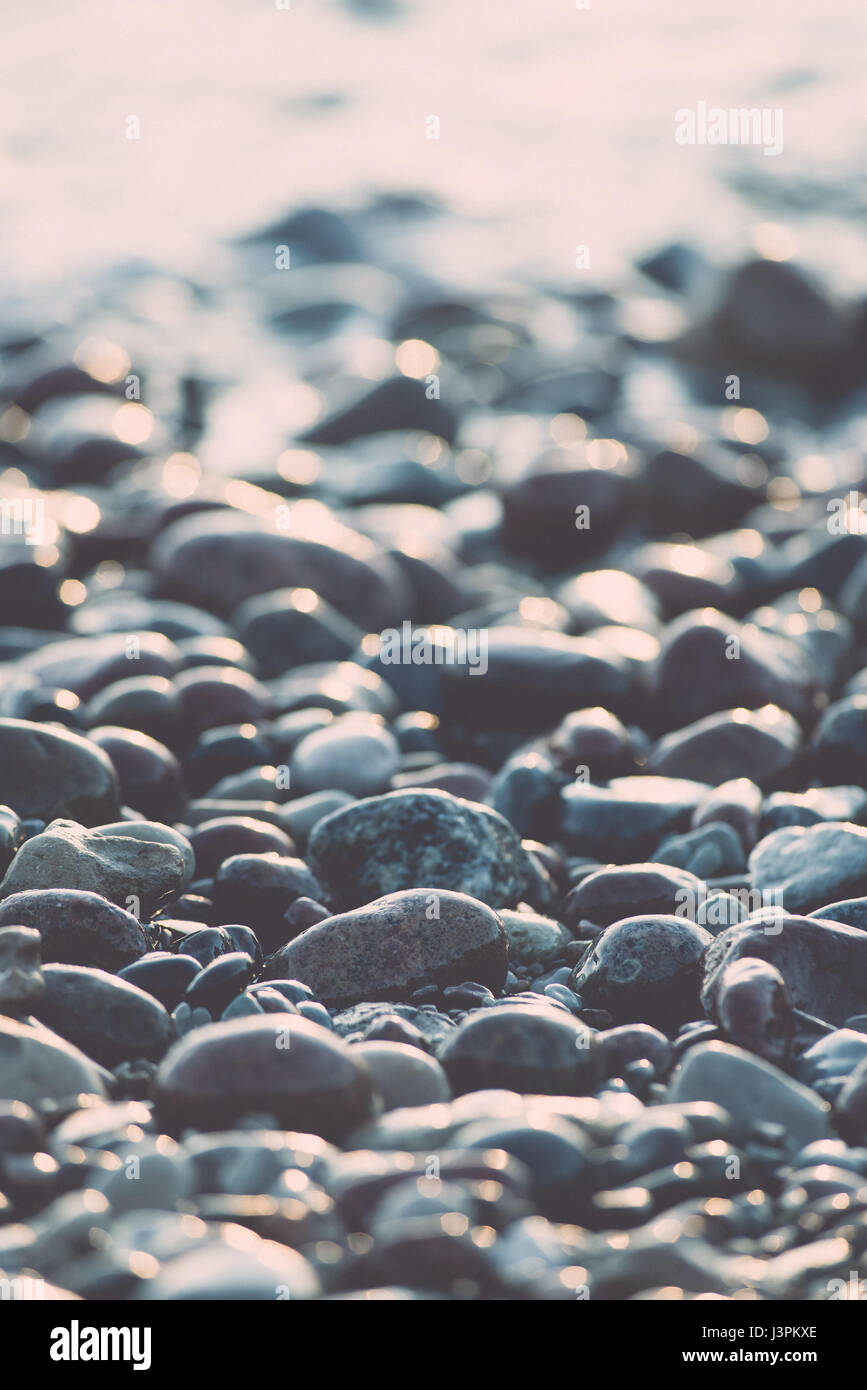 sun reflections on Stones on the beach and sea water in sunset light ...