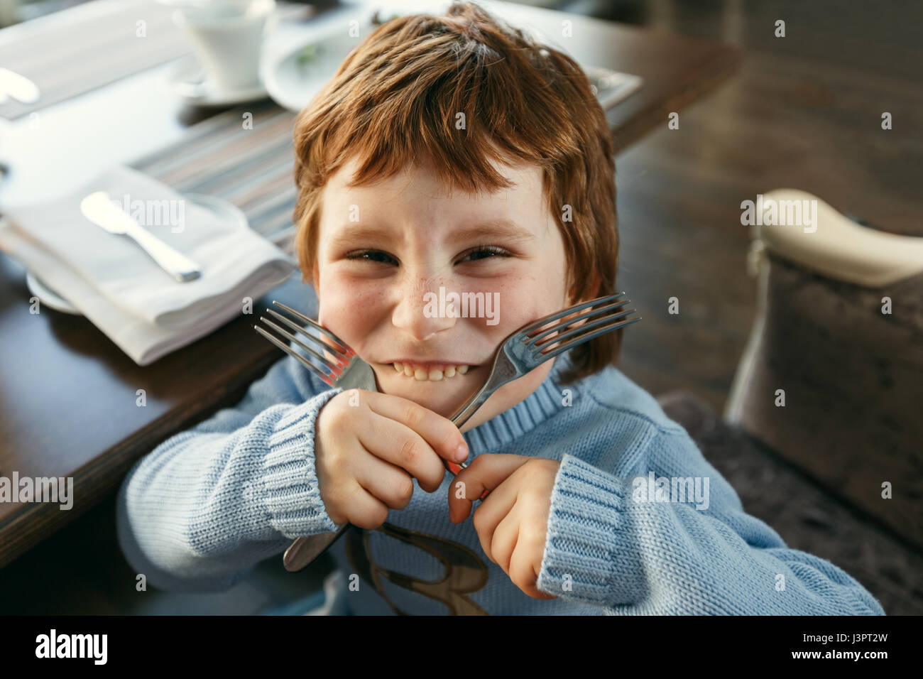 Little red haired boy playing the ape with two forks in a restaurant ...