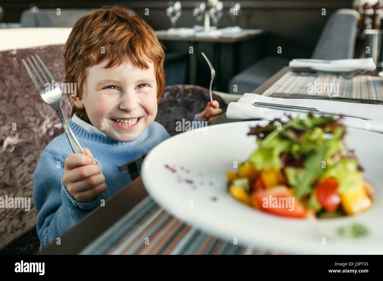 Little red haired boy playing the ape with two forks while eating salad ...