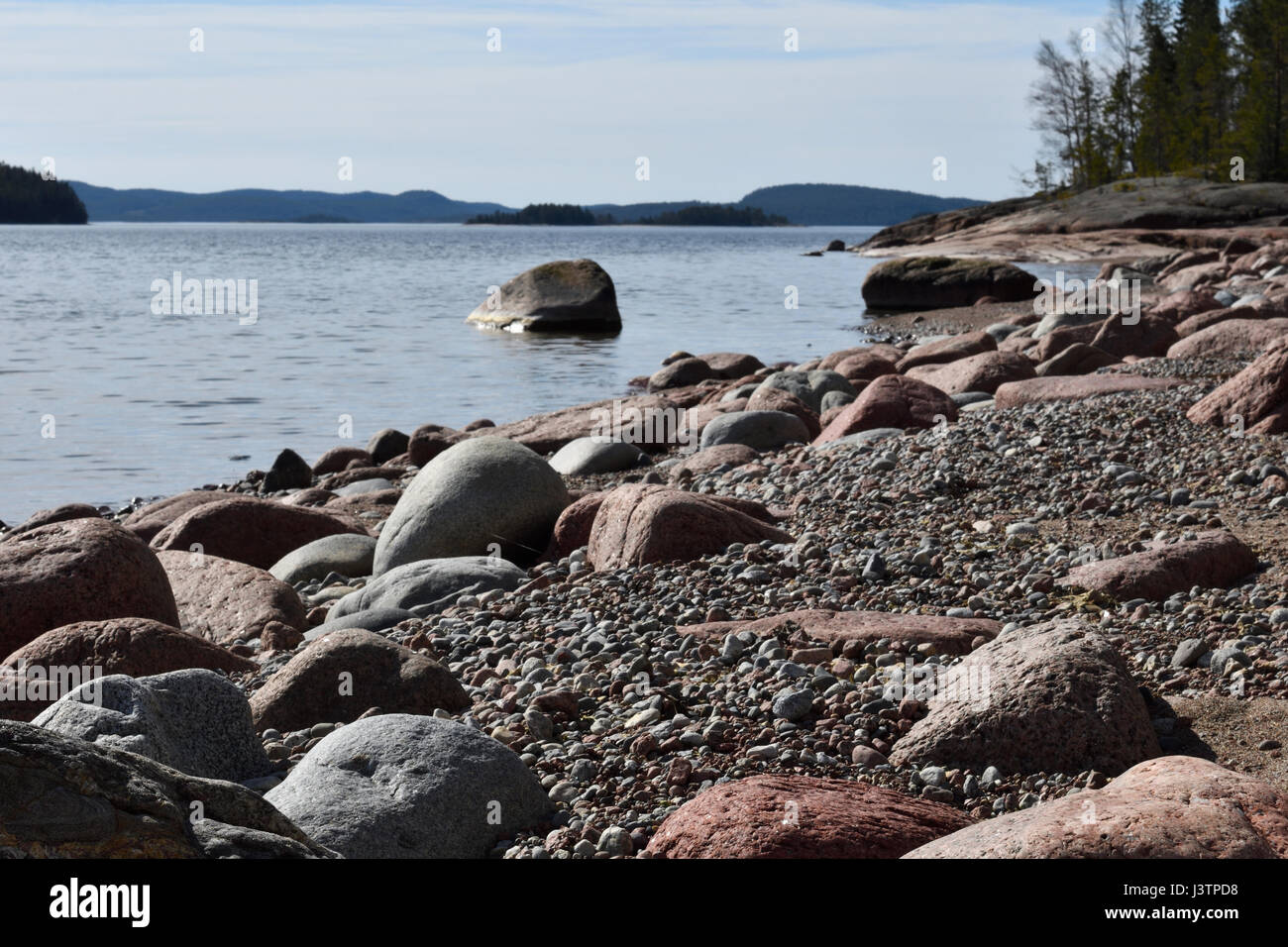 Shore with focus soft rounded granite stones in foreground and sea with ...