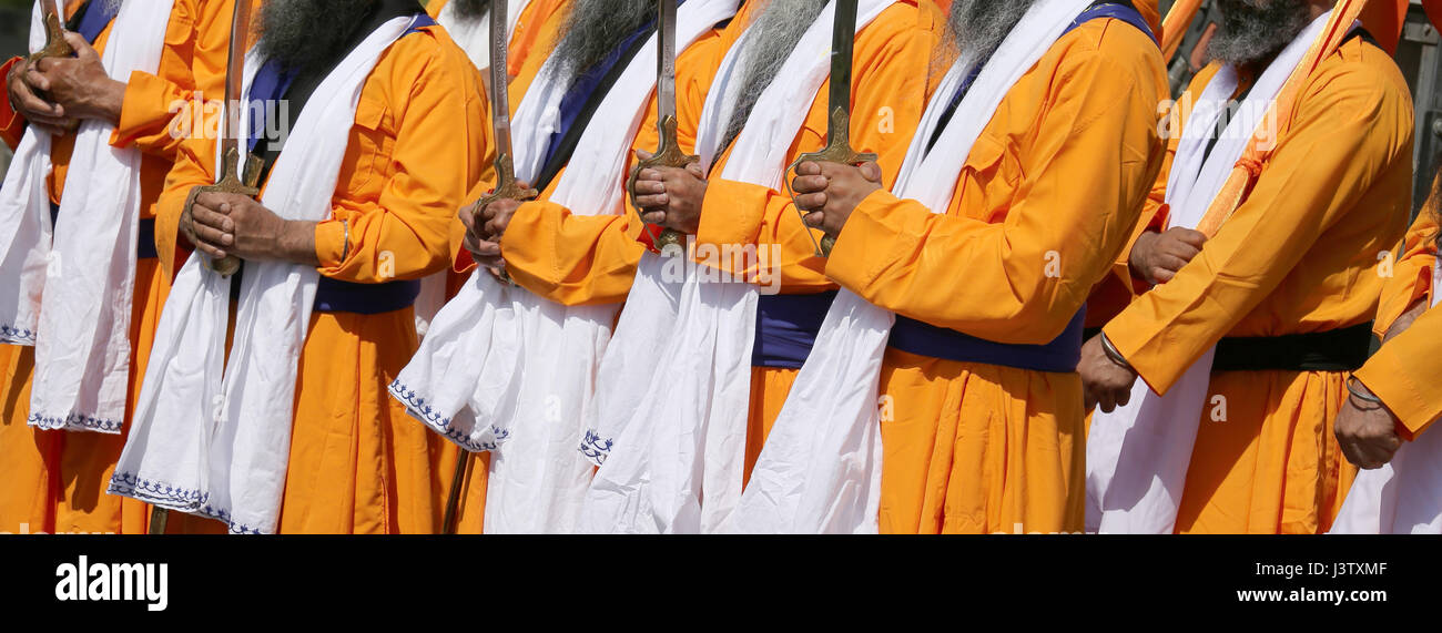 many men sikh with traditional orange clothes and the swords on hands ...