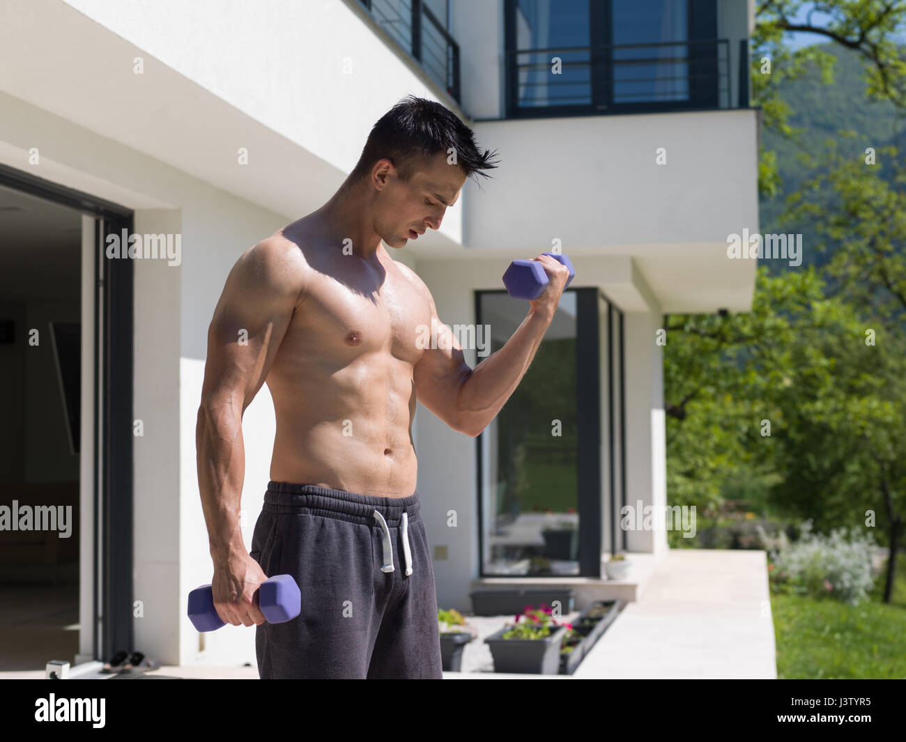 young handsome man doing morning exercises in front of his luxury home ...