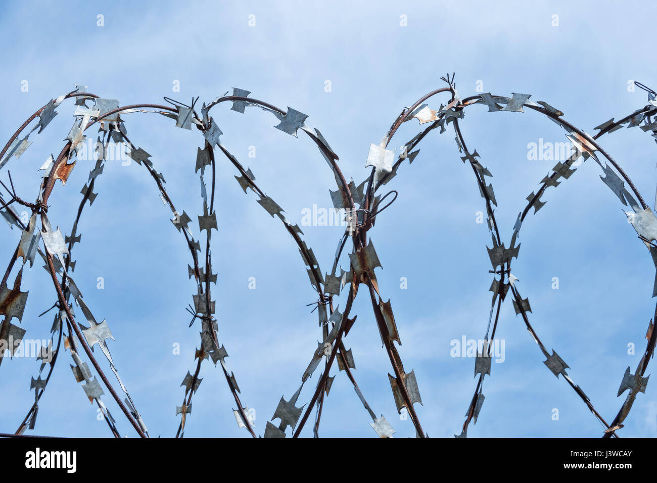 Rusty barbed wire with blades twisted into a spiral against the blue ...