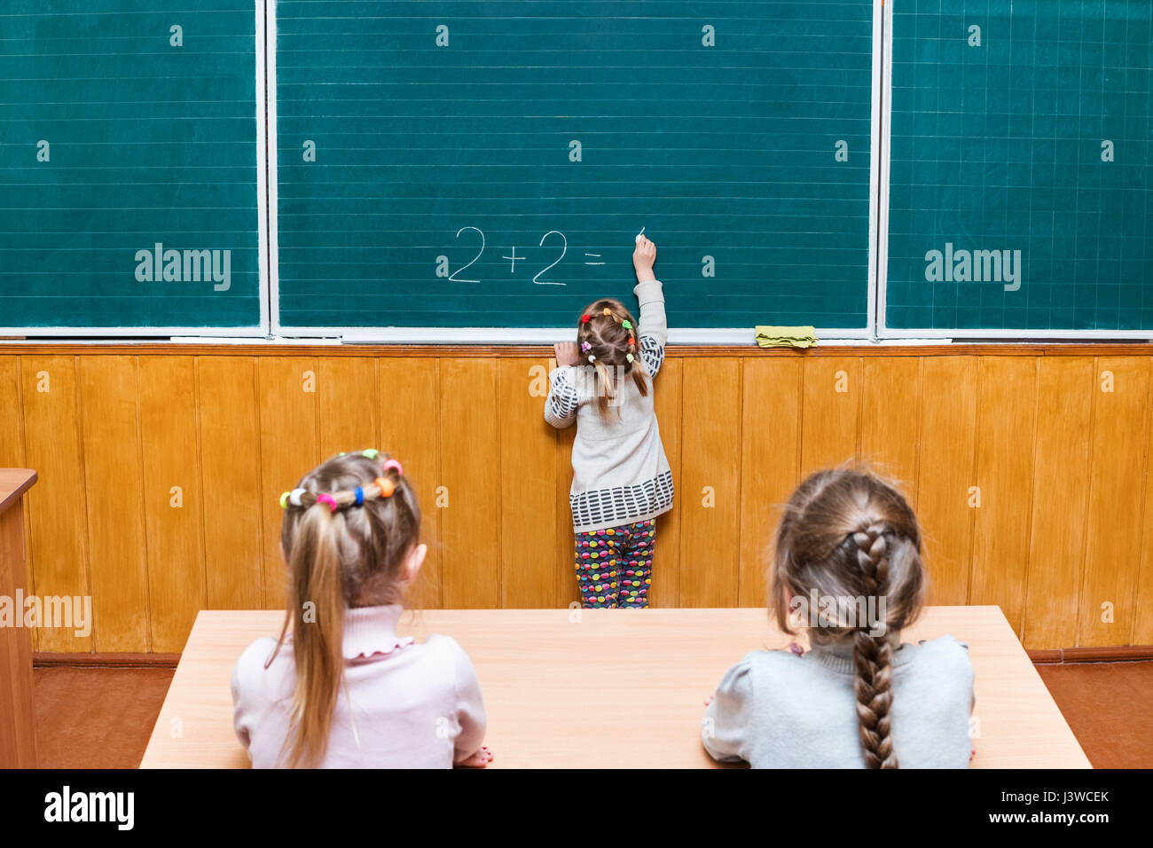 Little girl in the school class standing at the blackboard solves an ...