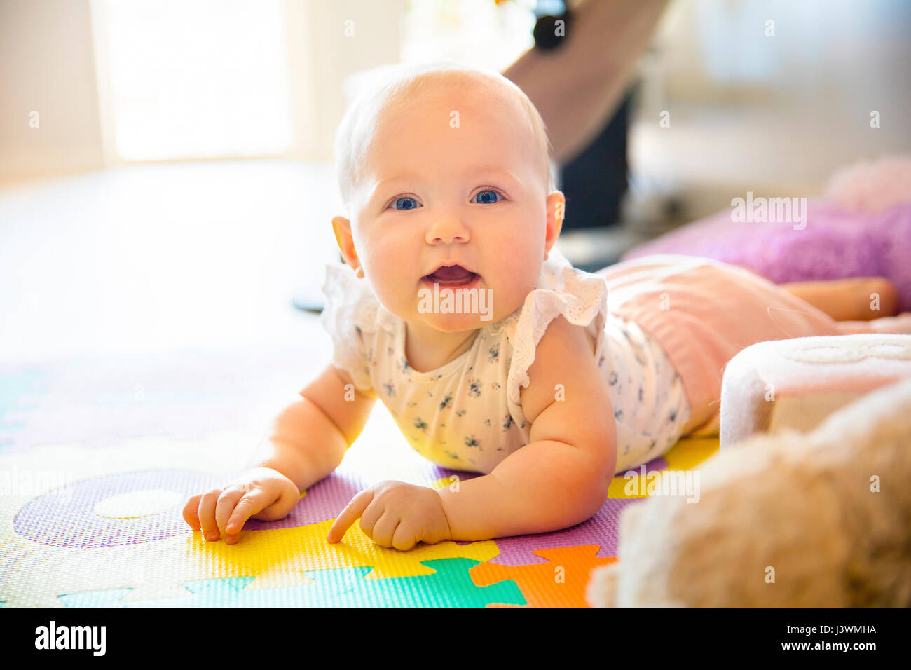 Smiling baby girl with blue eyes playing on the floor with toys on a ...