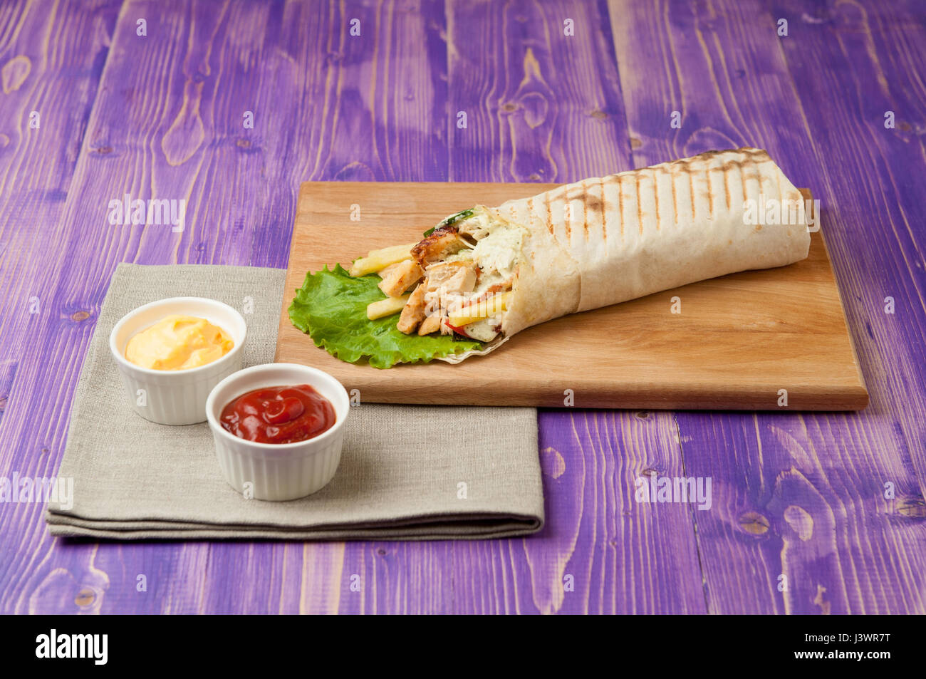 Arabic shawarma on wooden board and two white cups with ketchup and ...