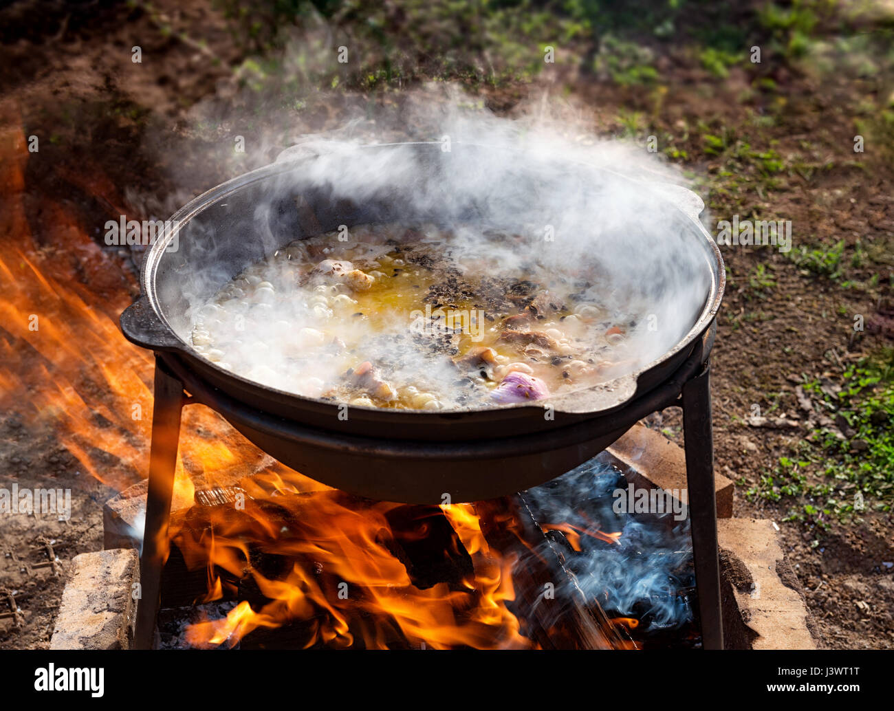 Cooking pilaf in a large cauldron with a strong steaming on an open ...
