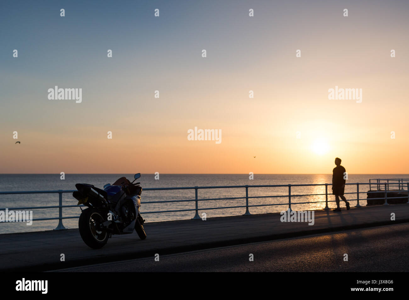 A silhouetted person walking and a motorcycle parked along a promenade ...