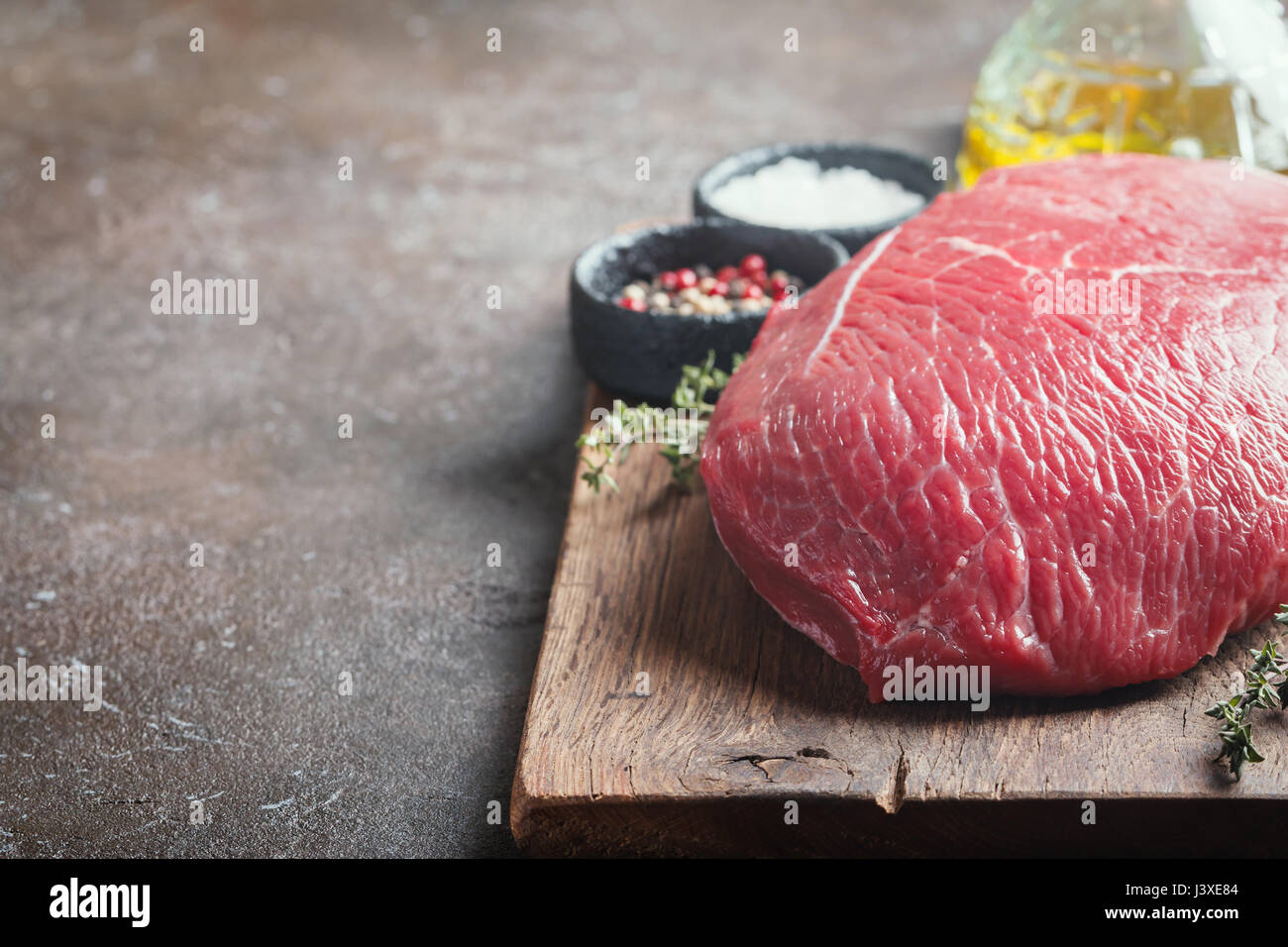 big cut of raw beef meat with thyme, garlic and spices over dark brown ...