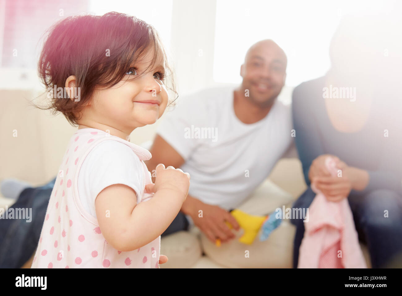 Baby girl toddling in living room with parents watching Stock Photo - Alamy