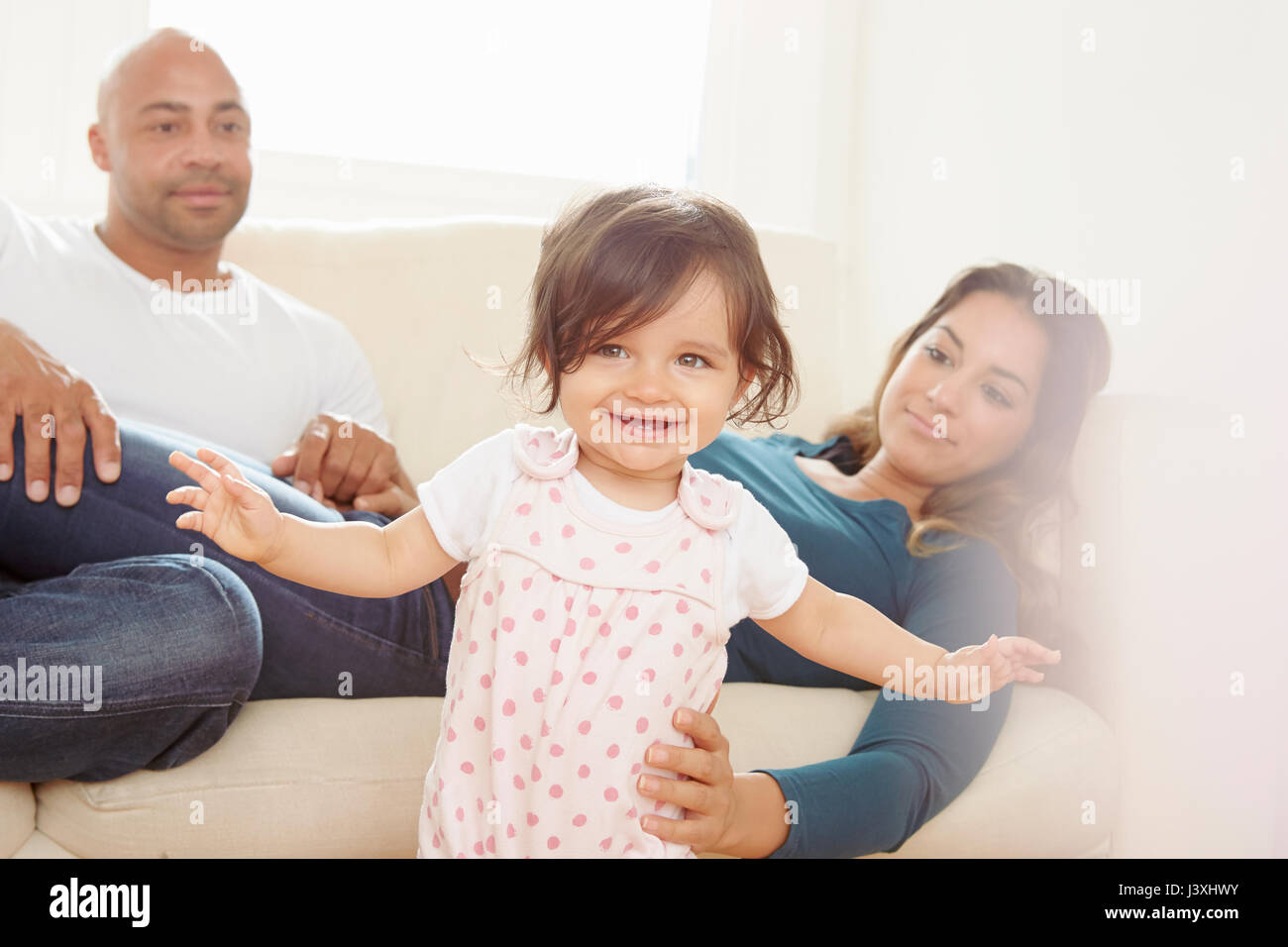 Mother on sofa giving baby daughter helping hand while toddling Stock ...