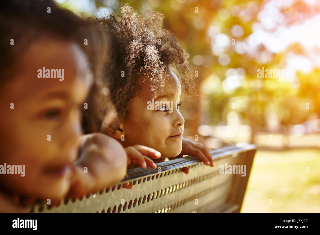 Two young sisters looking peering over bench Stock Photo - Alamy