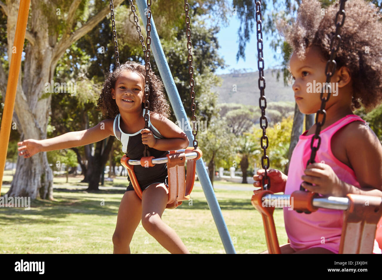 Two young sisters playing on park swings Stock Photo - Alamy